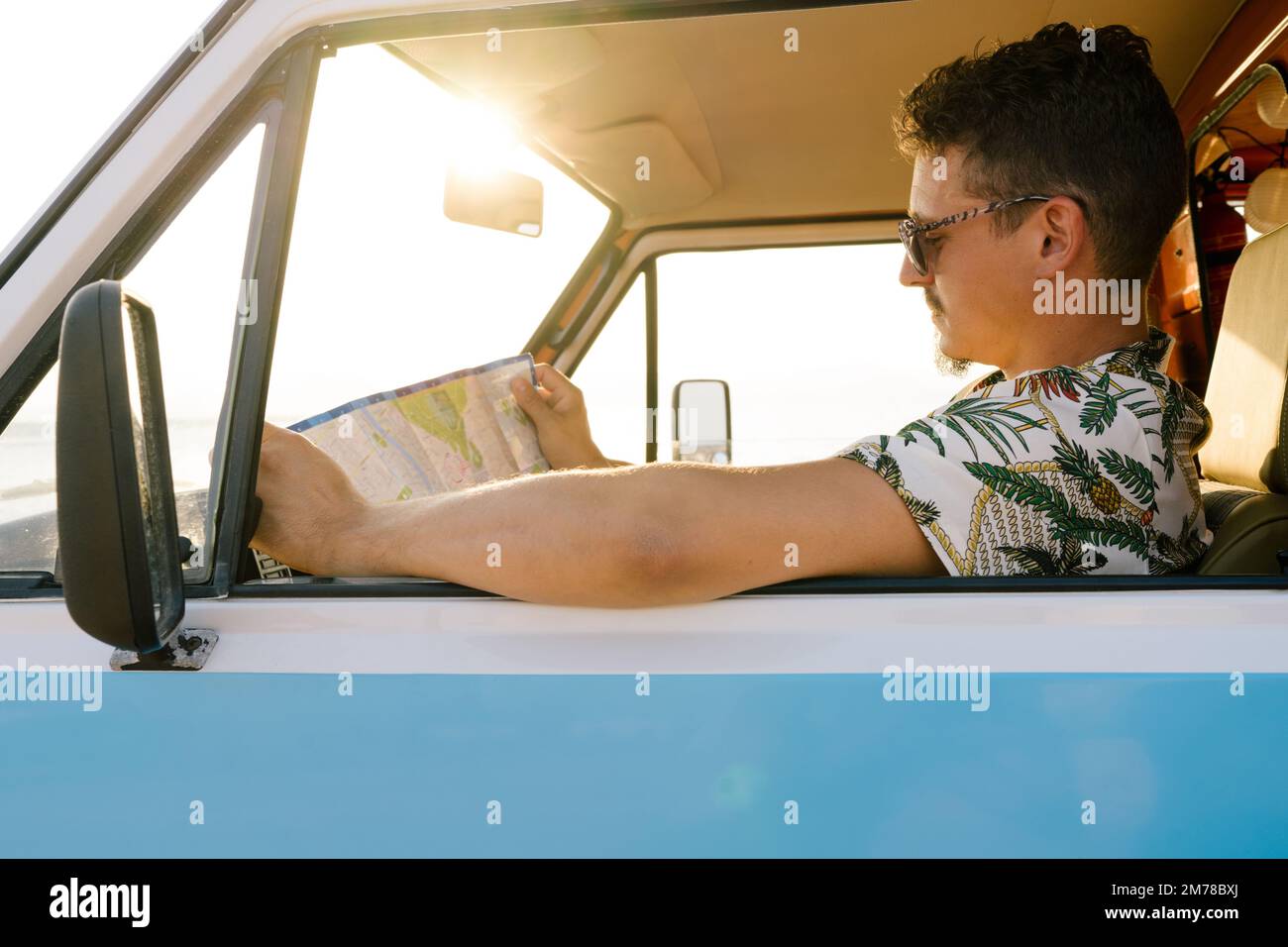 Profile of a man using a map while driving a camper van during sunset ...