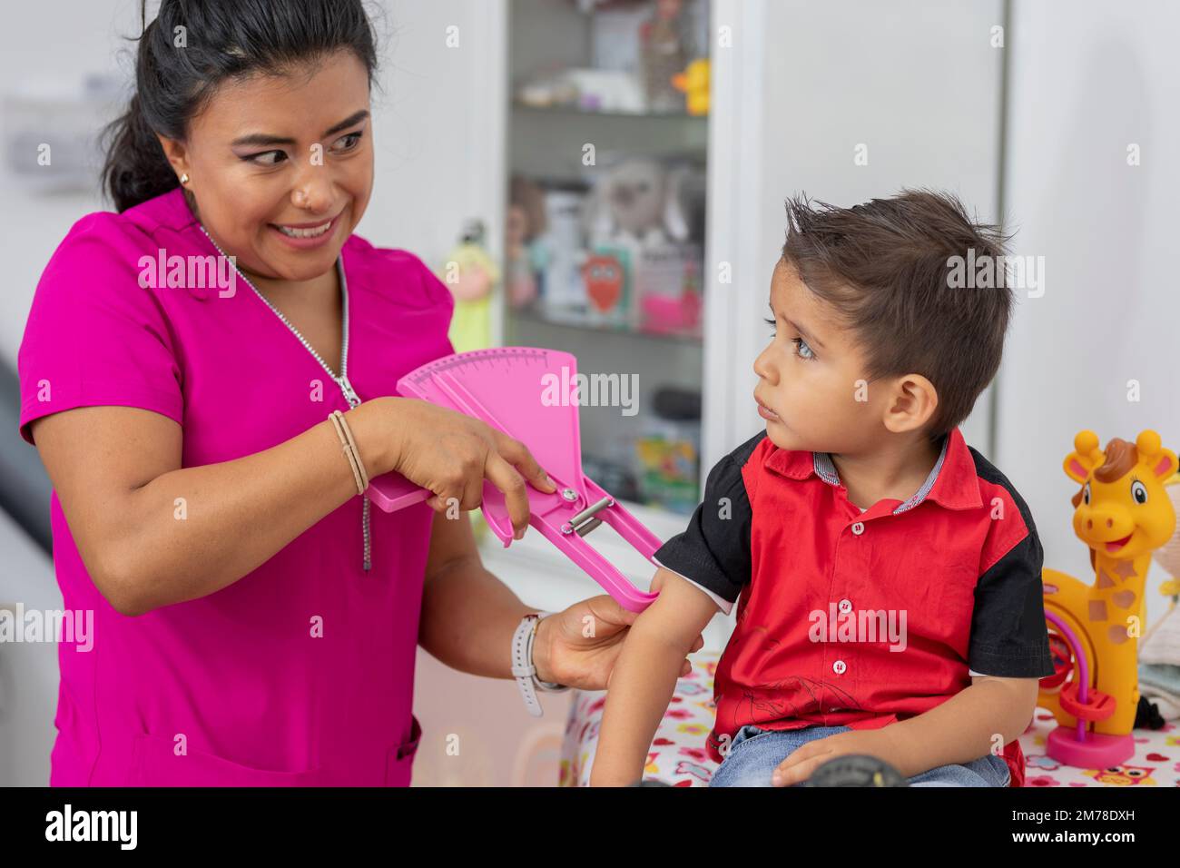 Female pediatrician doctor measuring the fat of a child with a caliper ...