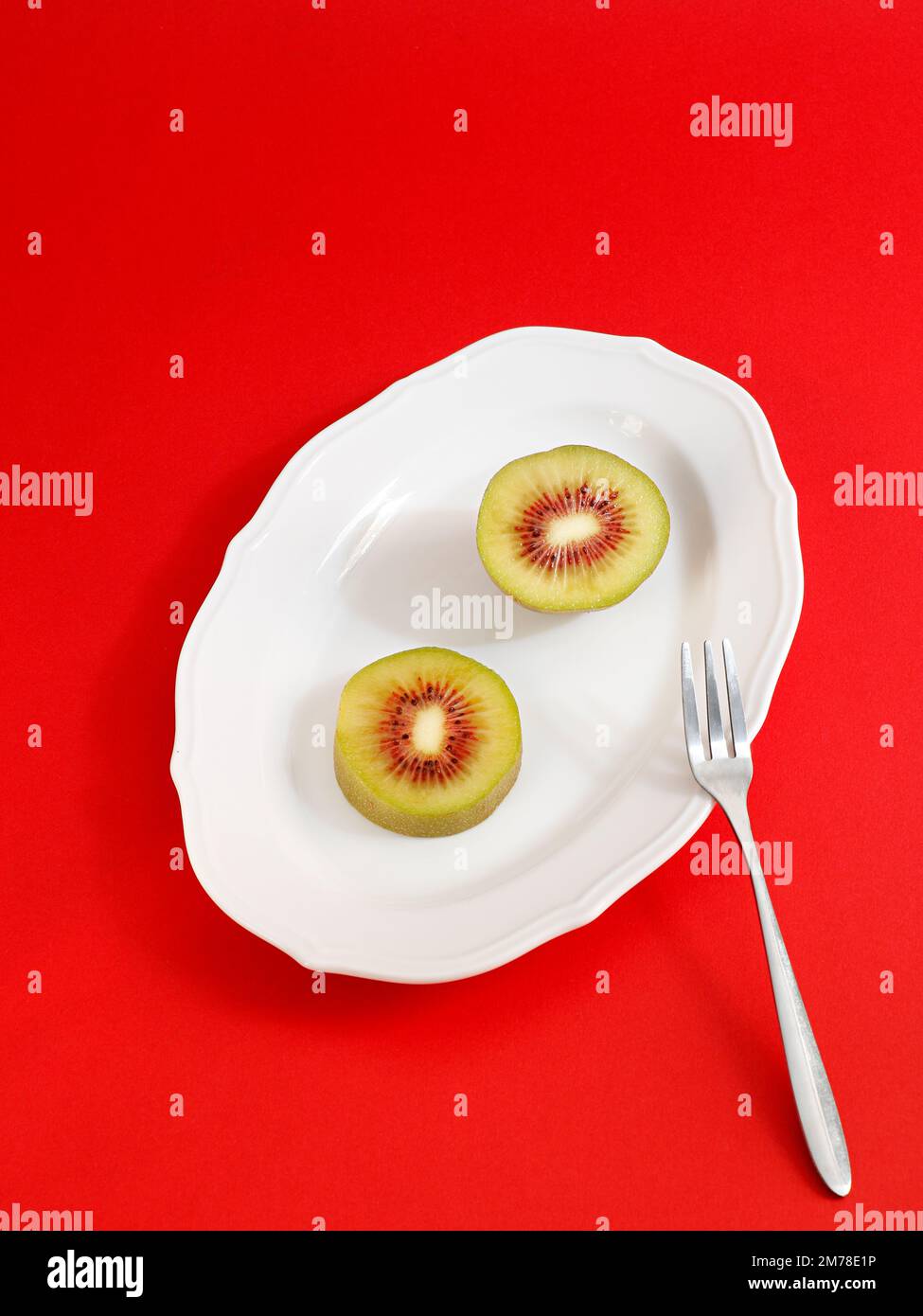 A vertical shot of kiwi fruits cut in halves in white plate on red ...