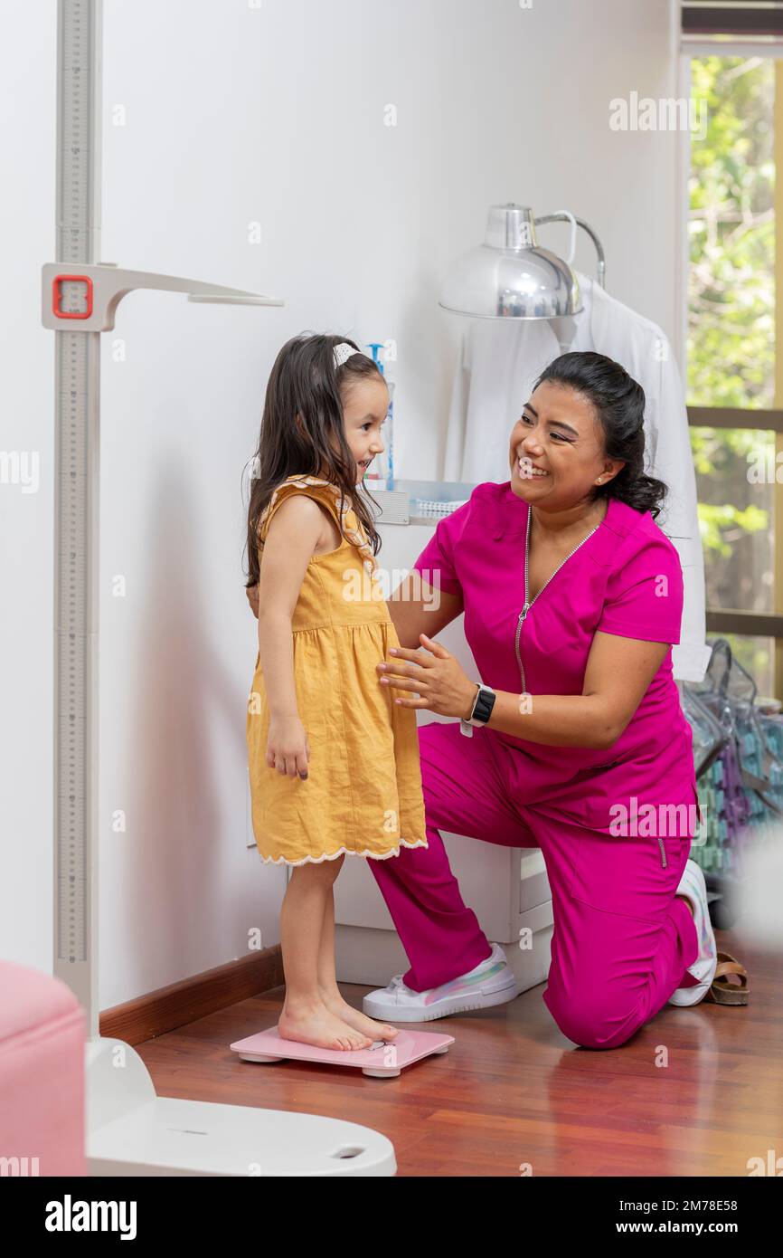 Pediatrician doctor weighing a girl on a floor scale, in her office ...