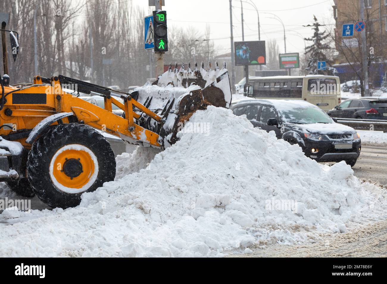 The blade of a communal tractor clears piles of snow from a city street ...