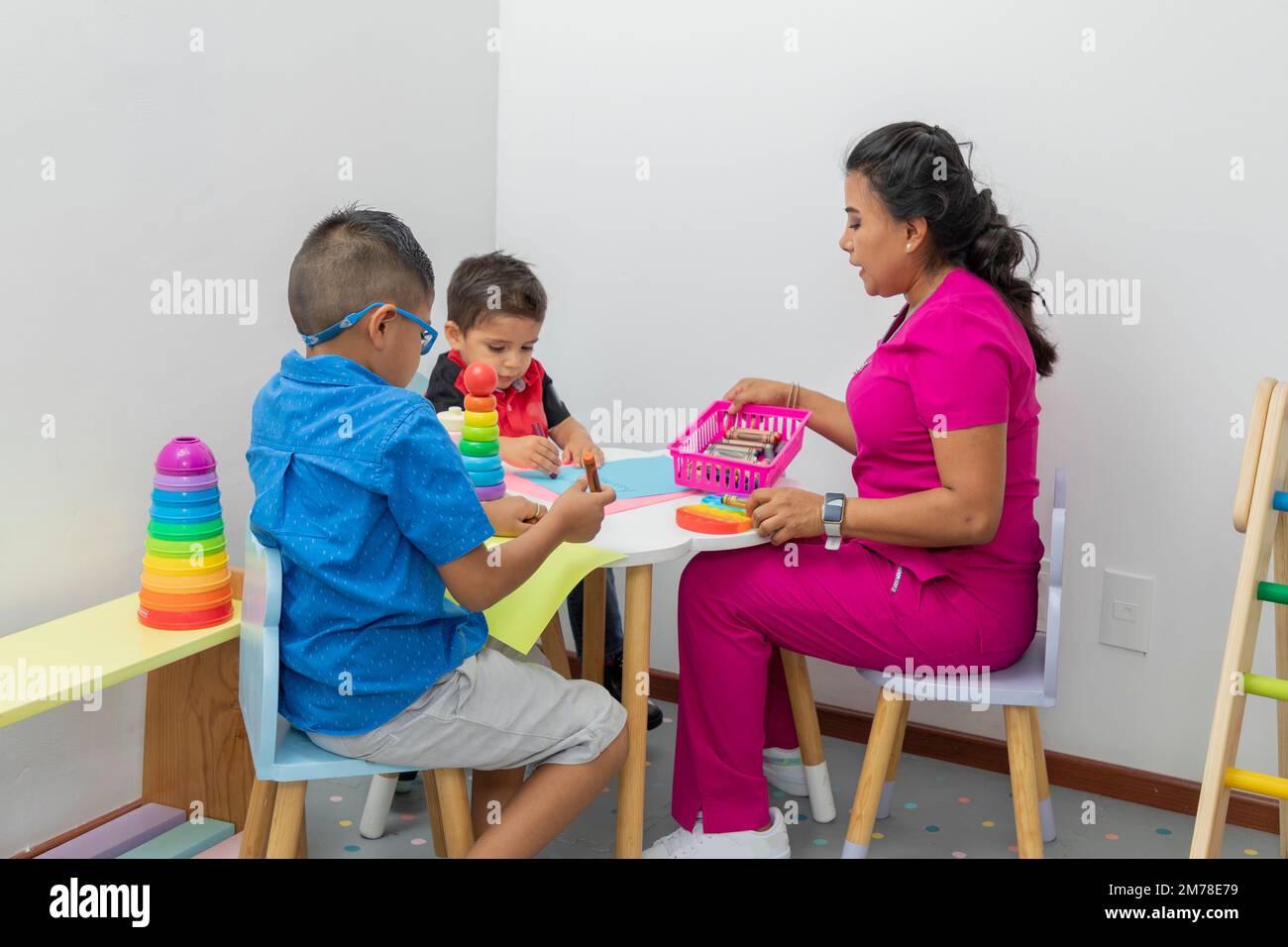 Latina pediatrician doctor, playing with two children at a table with ...