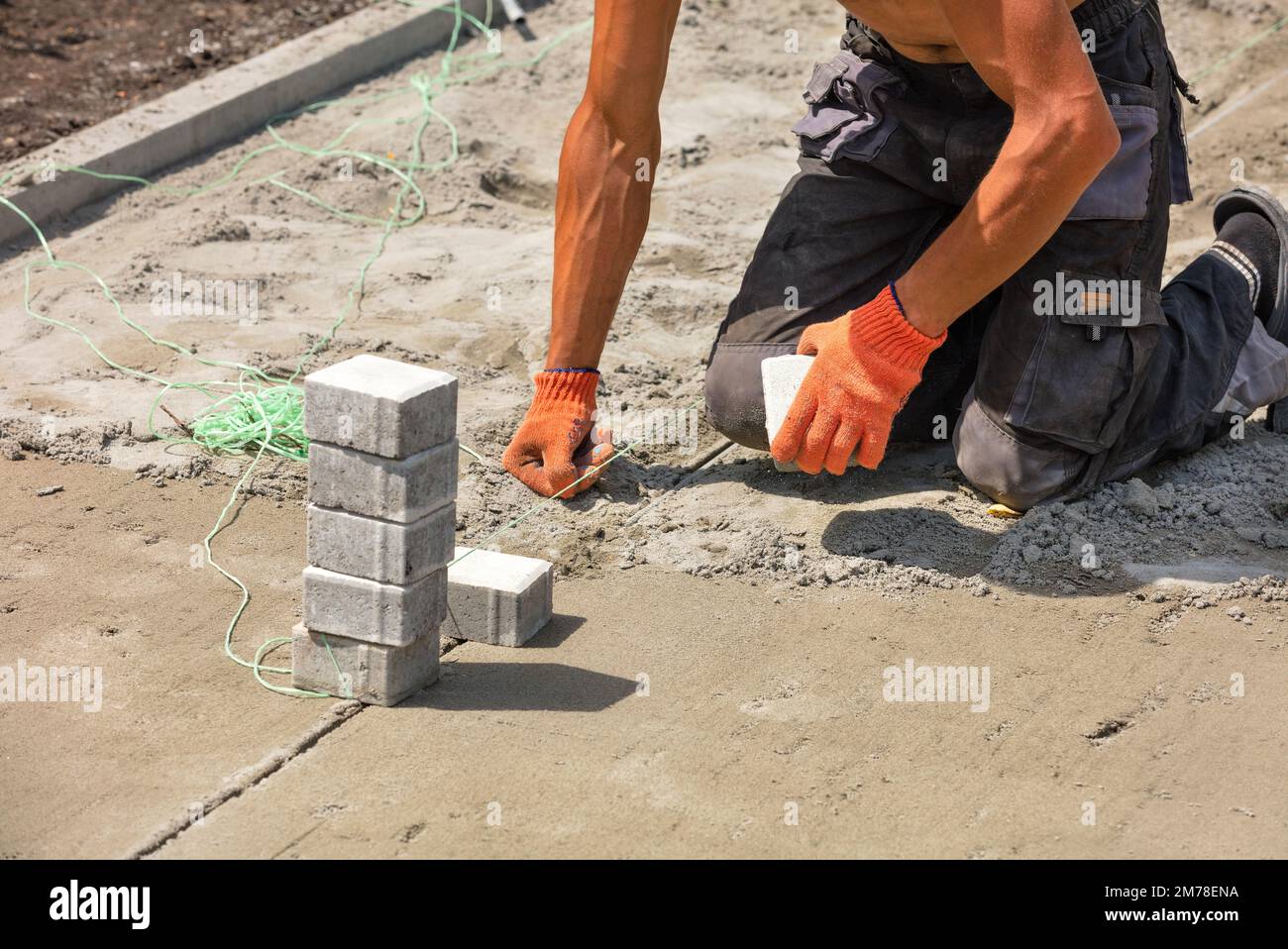 A worker installs nylon string to lay paving slabs on a bright sunny ...