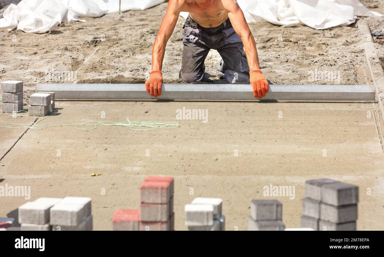 A worker levels the sand base at a paving slab laying workplace on a ...