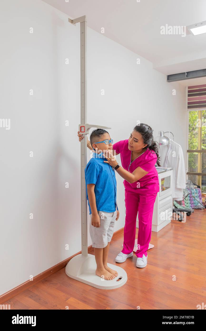 Latina pediatrician measuring a child with a wall ruler in her office ...