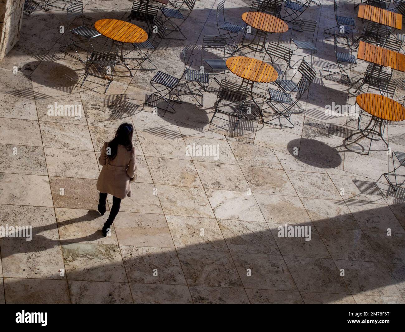 A woman walking through an empty outdoor dining area with marble floors ...