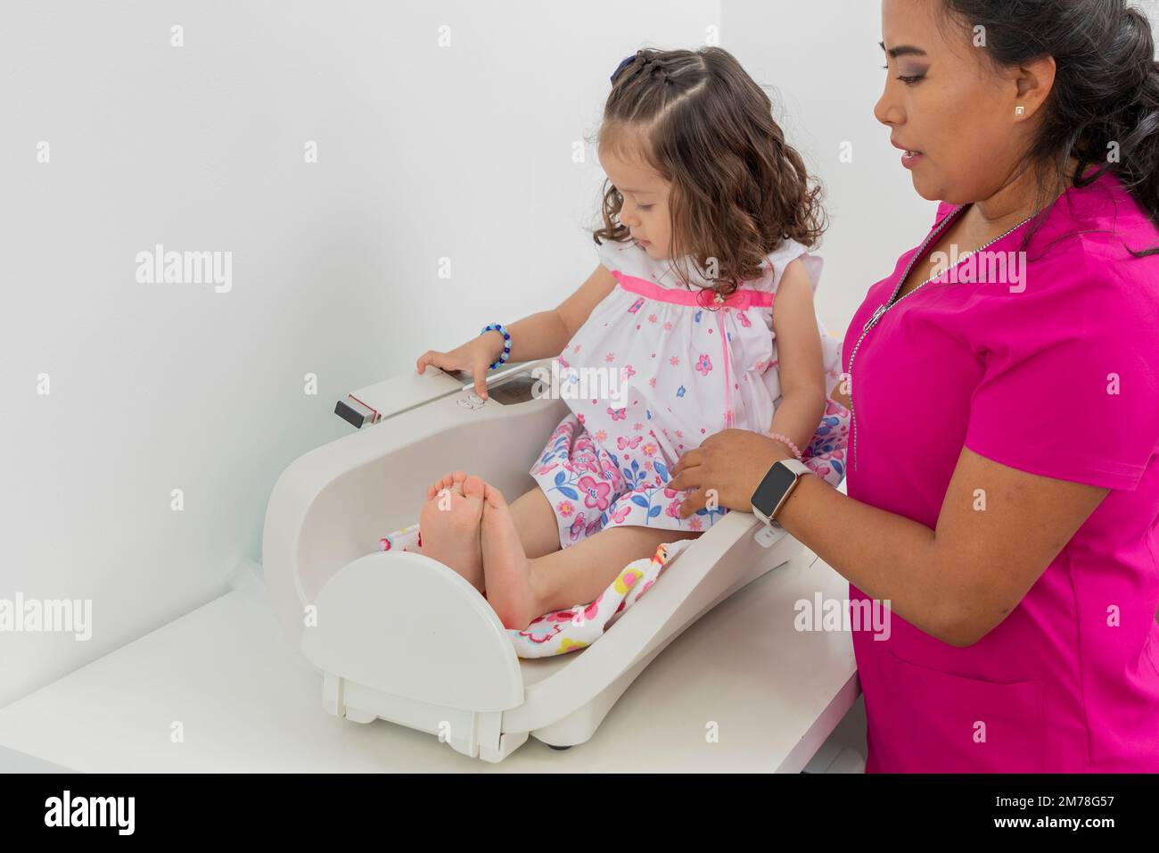 Girl sitting on a modern scale, while the pediatrician weighs her, in ...