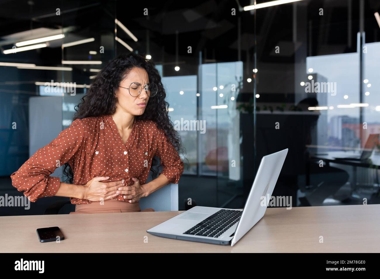 Abdominal pain at the workplace. A young Latin American woman is ...