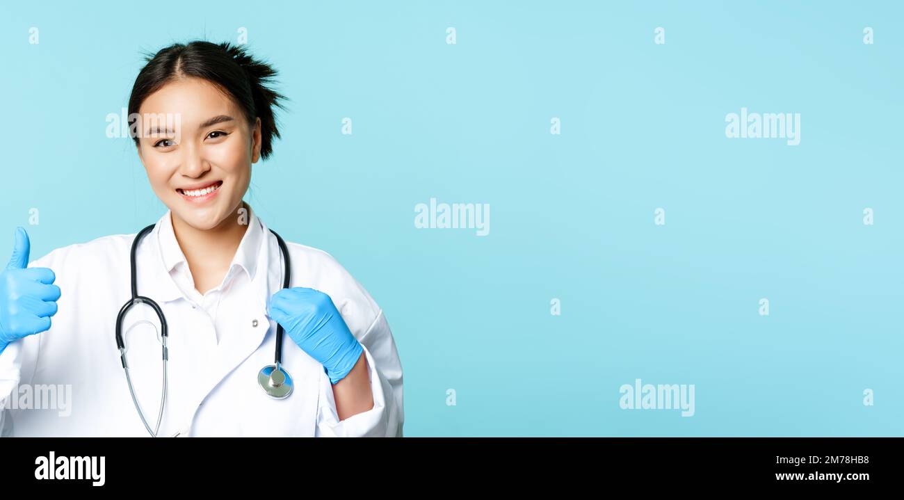 Smiling asian woman therapist, physician with stethoscope shows thumbs ...
