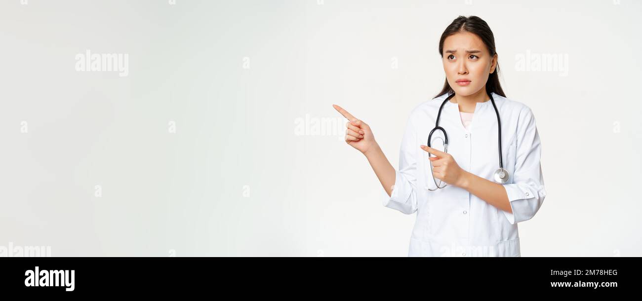 Skeptical female doctor, concerned nurse pointing and looking left with ...