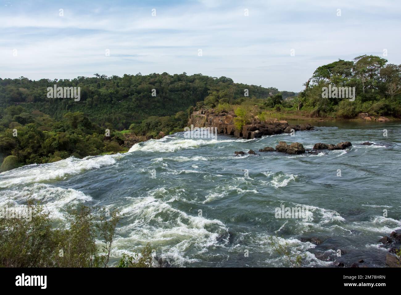 A landscape scene of Iguazu waterfalls with wood trees with blue sky in ...