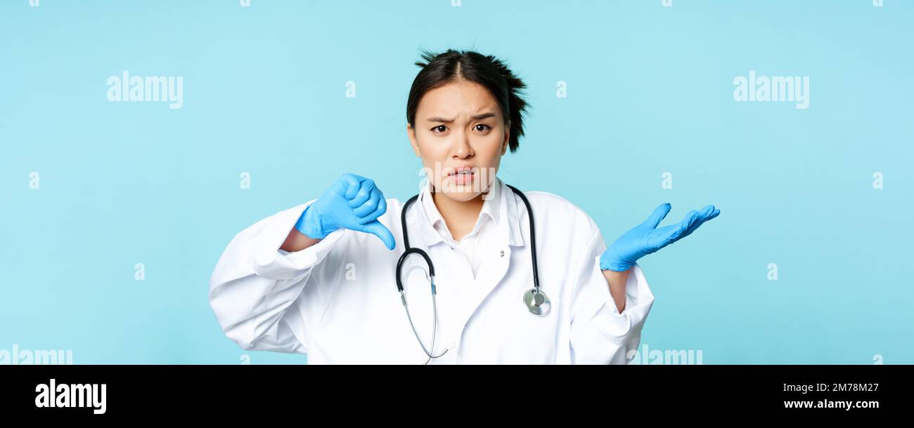 Frustrated asian doctor, nurse shows thumbs down and looking confused ...