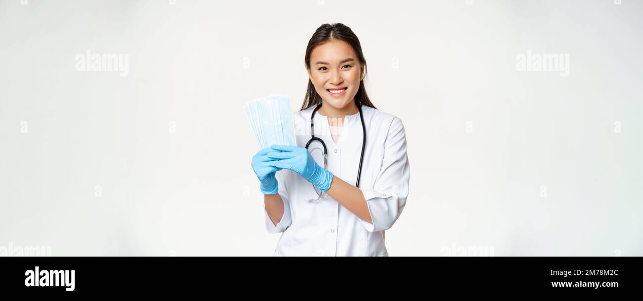 Smiling asian woman doctor, nurse showing medical face masks, wearing ...