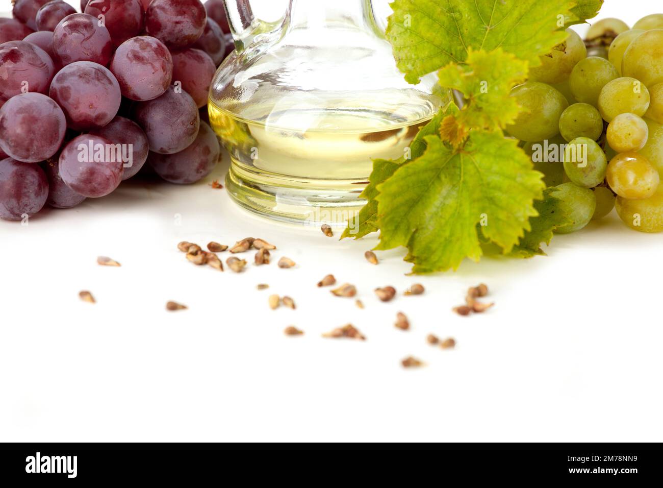 Grape seed oil on white background. The image also shows light grapes ...