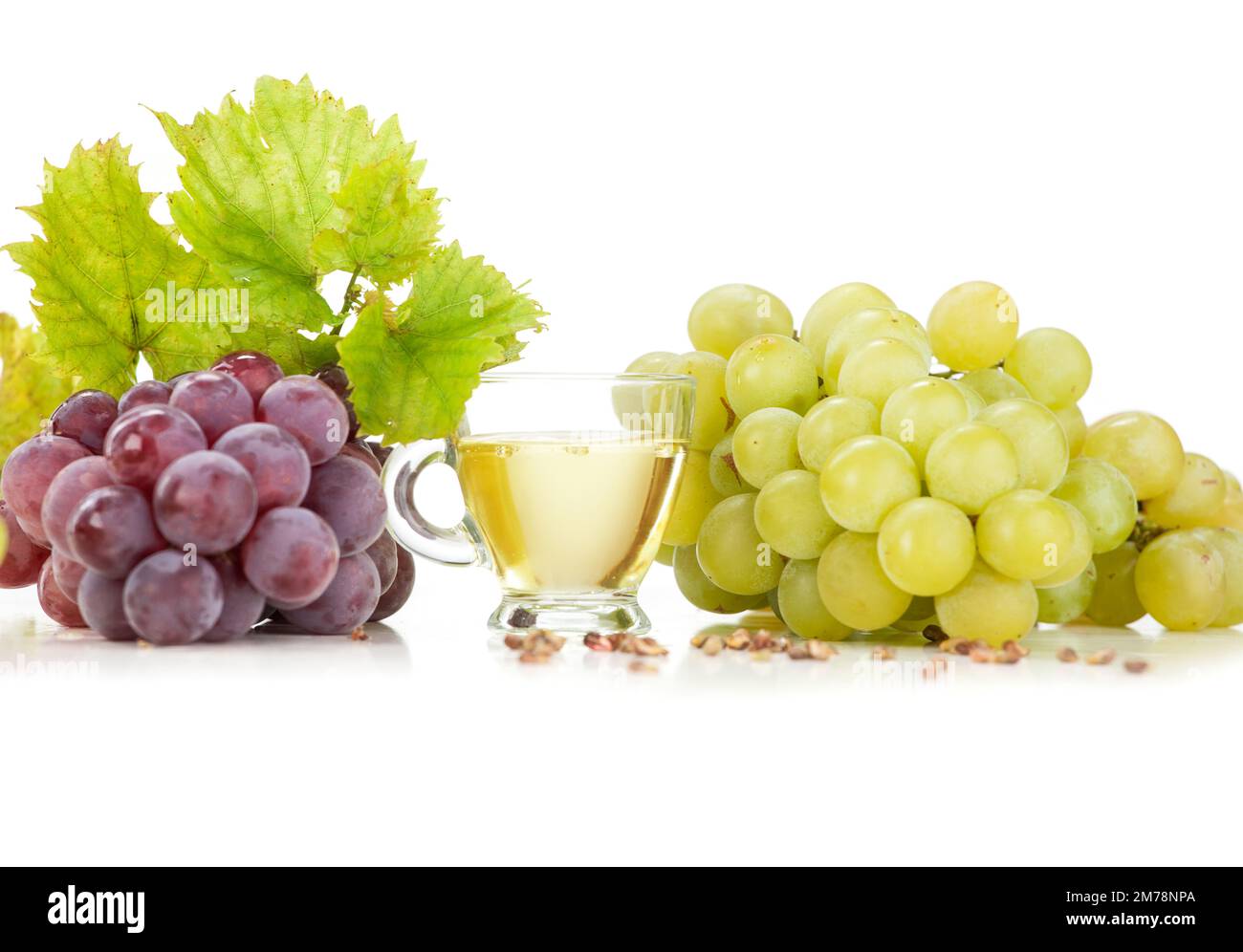Grape seed oil on white background. The image also shows light grapes and dark grapes arranged ...