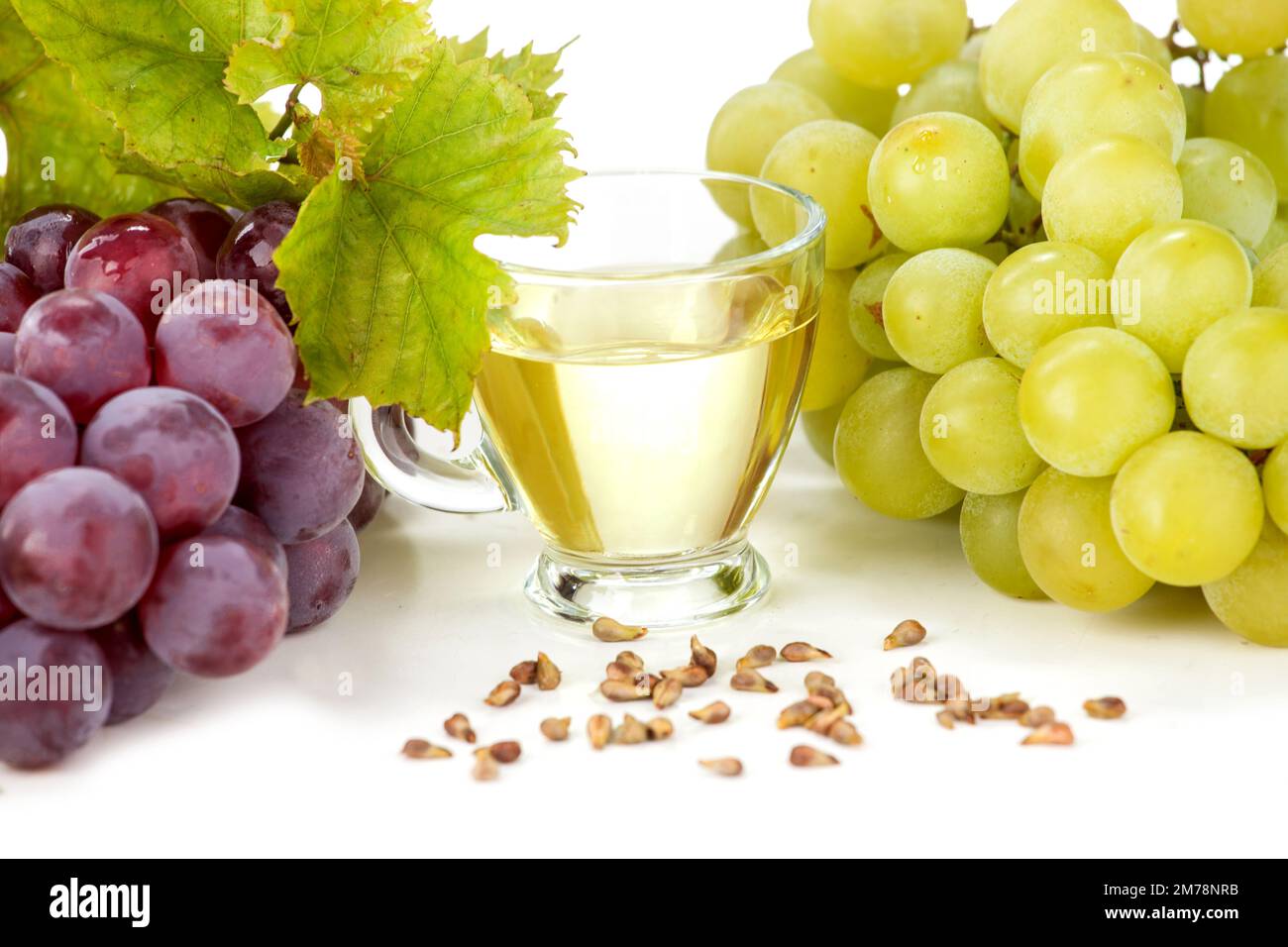 Grape seed oil on white background. The image also shows light grapes ...