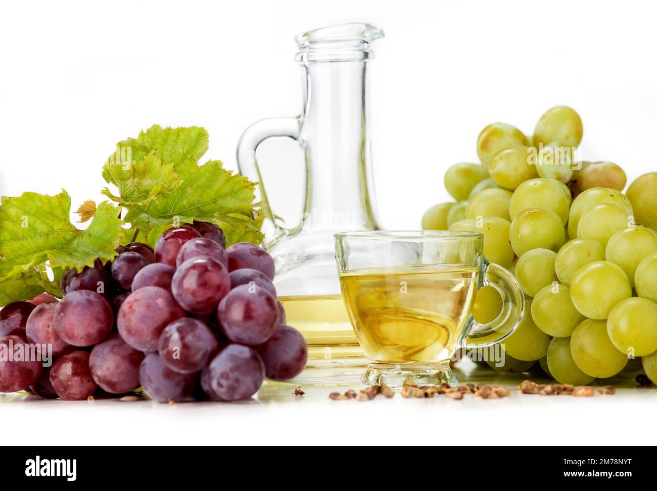 Grape seed oil on white background. The image also shows light grapes ...