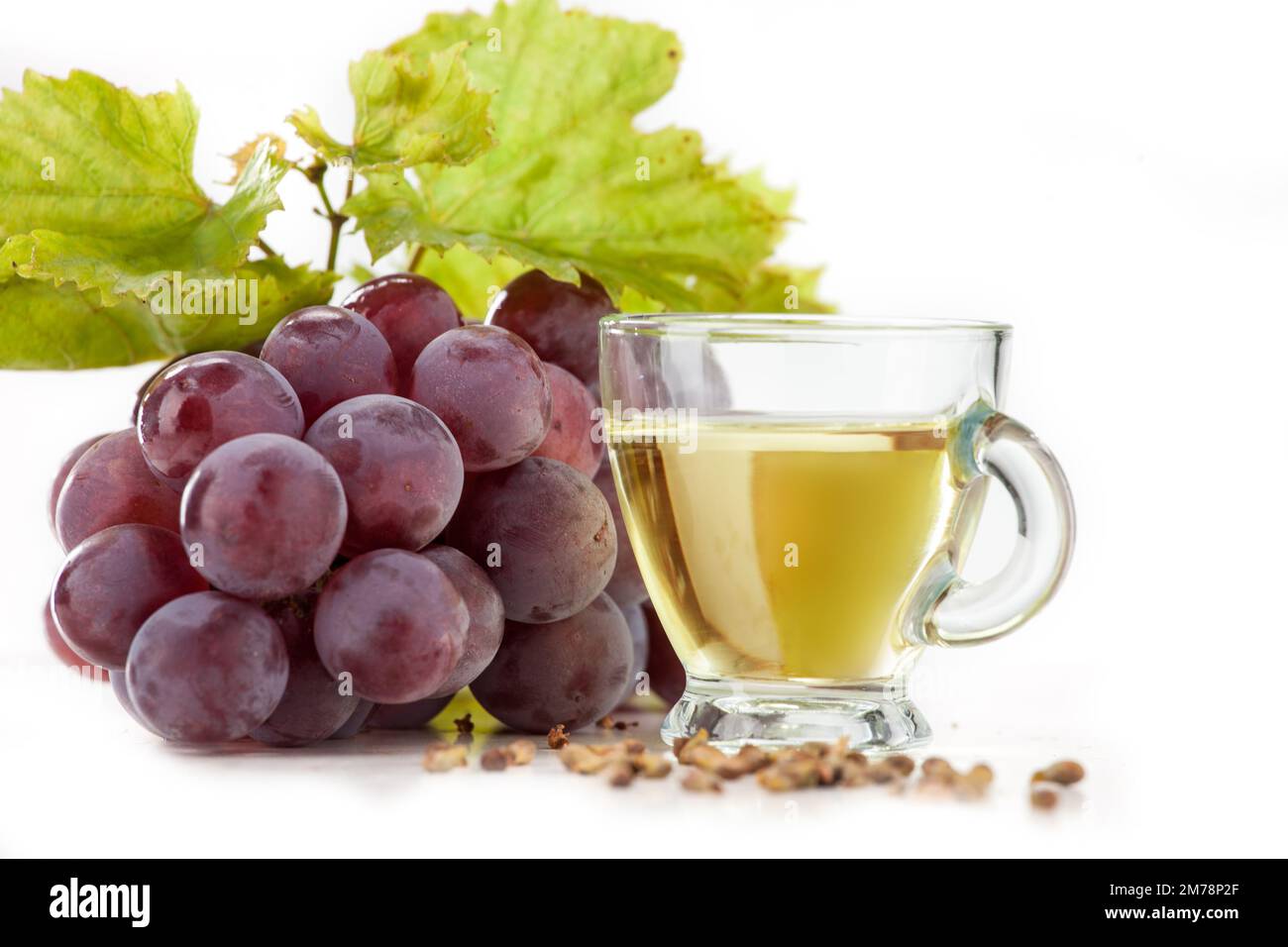 Grape seed oil on white background. The image also shows light grapes ...