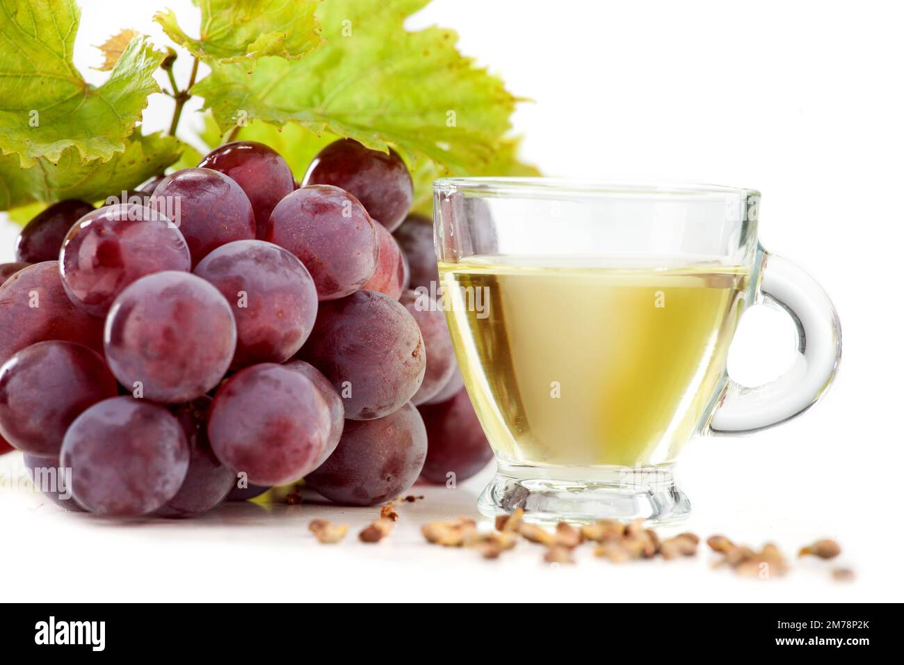 Grape seed oil on white background. The image also shows light grapes ...