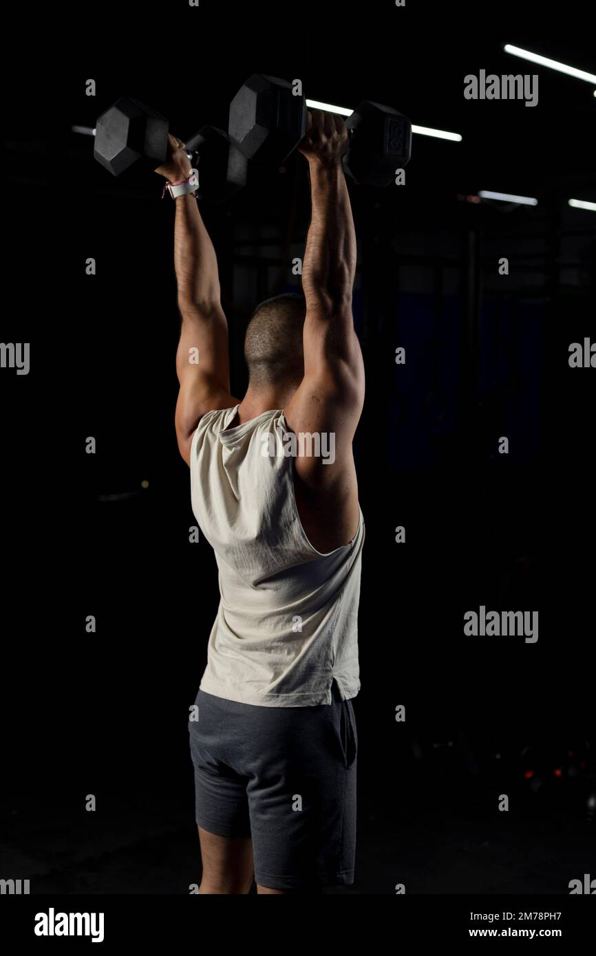 vertical shot of a muscular man from the side, pressing a pair of ...
