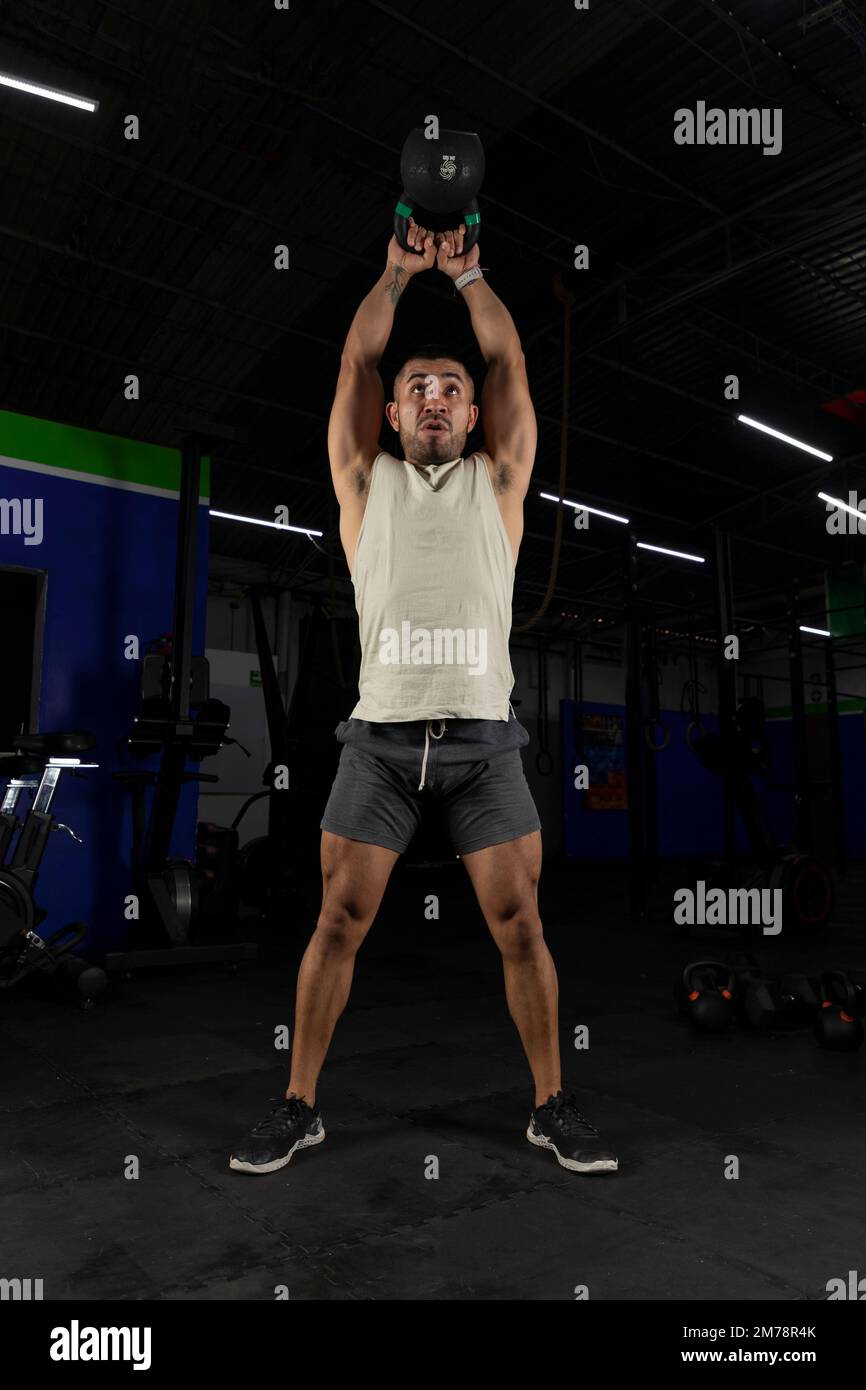 vertical photo of a latin man exercising with a kettlebell in a gym ...