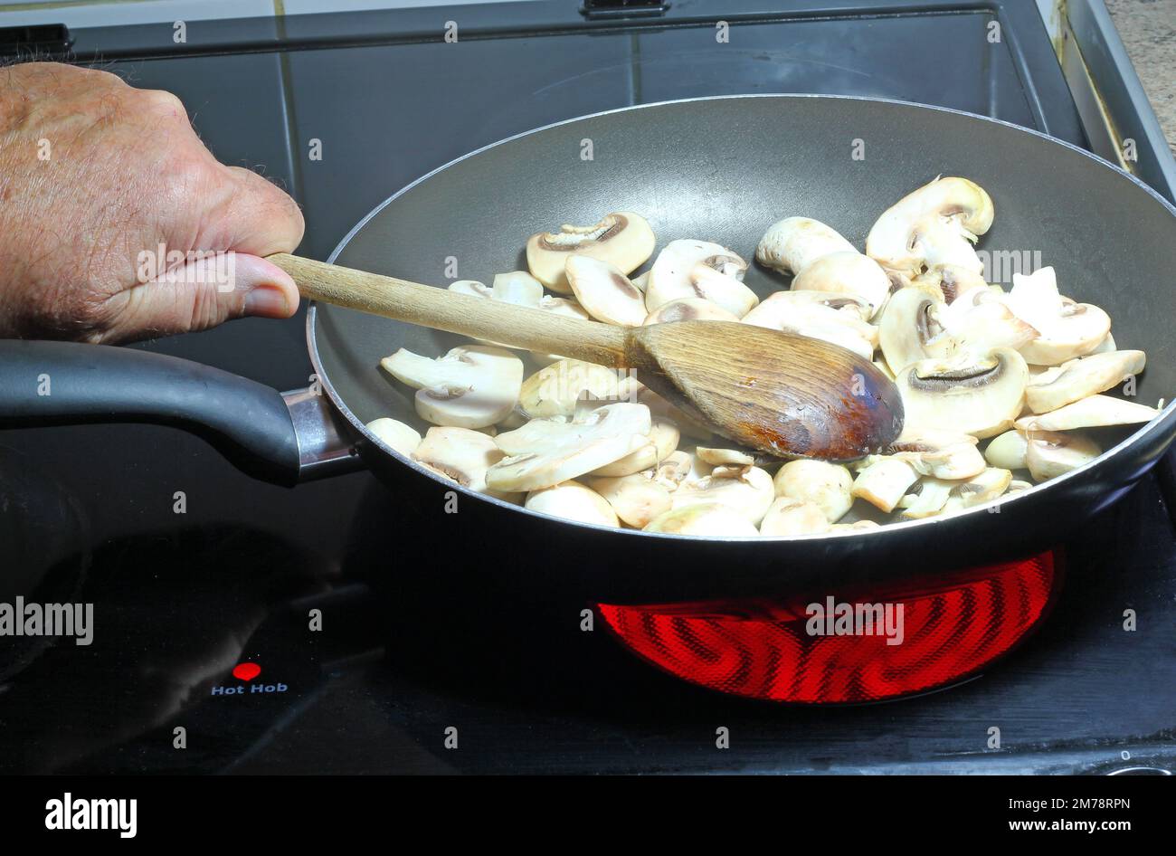 cooking mushrooms in a pan. Using wooden spoon to stir sliced mushrooms ...