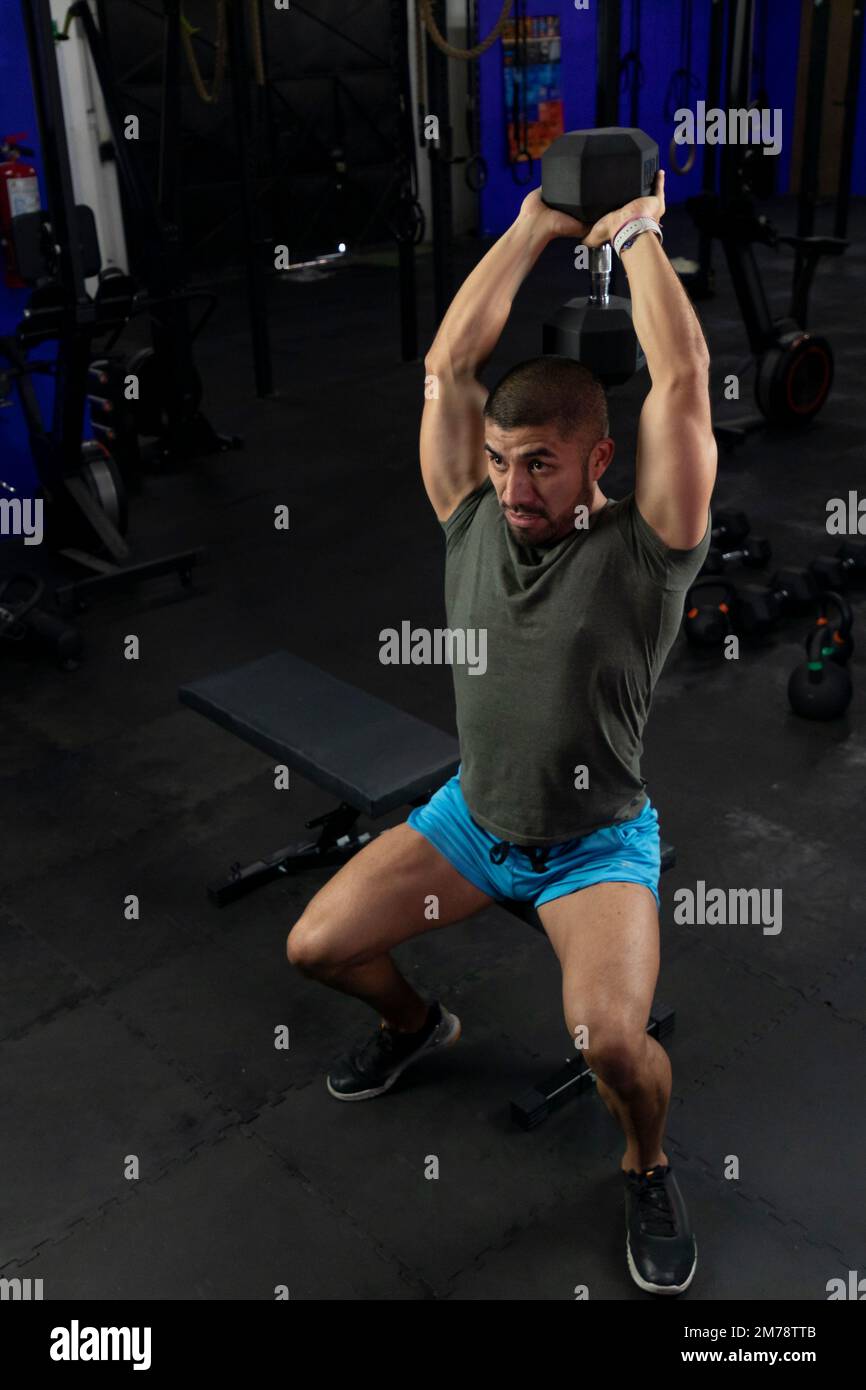 Muscular Latino man doing exercises for biceps sitting on a gym bench ...
