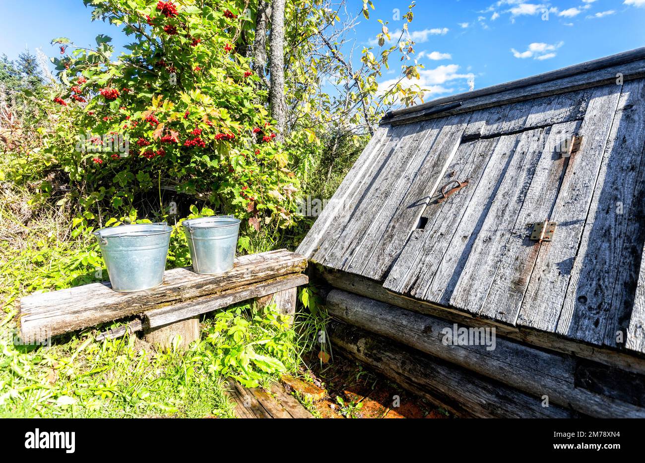 Metal buckets with water on a bench near a village wooden well on a ...