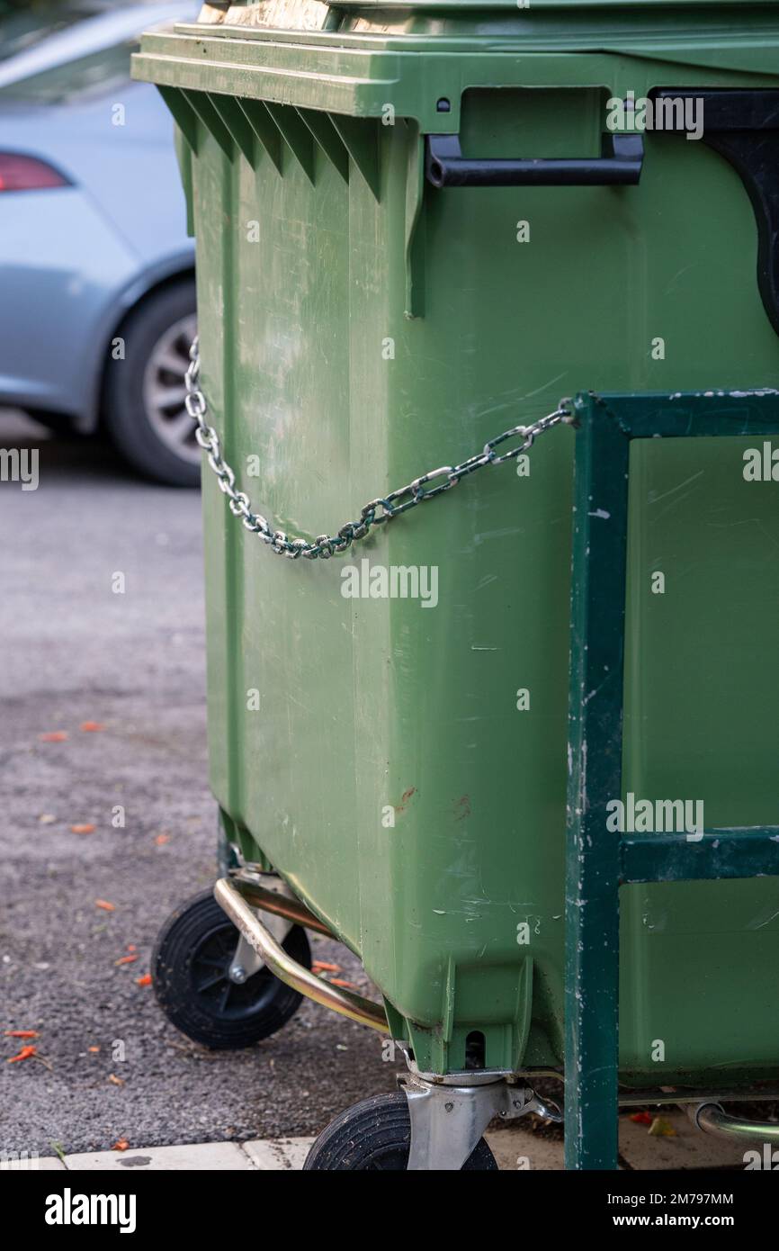 A large green plastic trash can. A bin secured with an iron chain ...