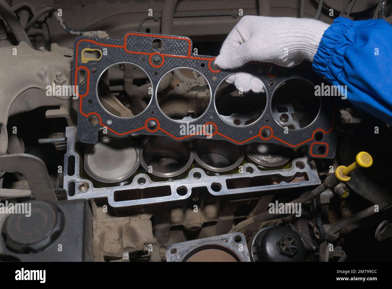 An auto mechanic holds a gasket over a car engine block with his hand ...