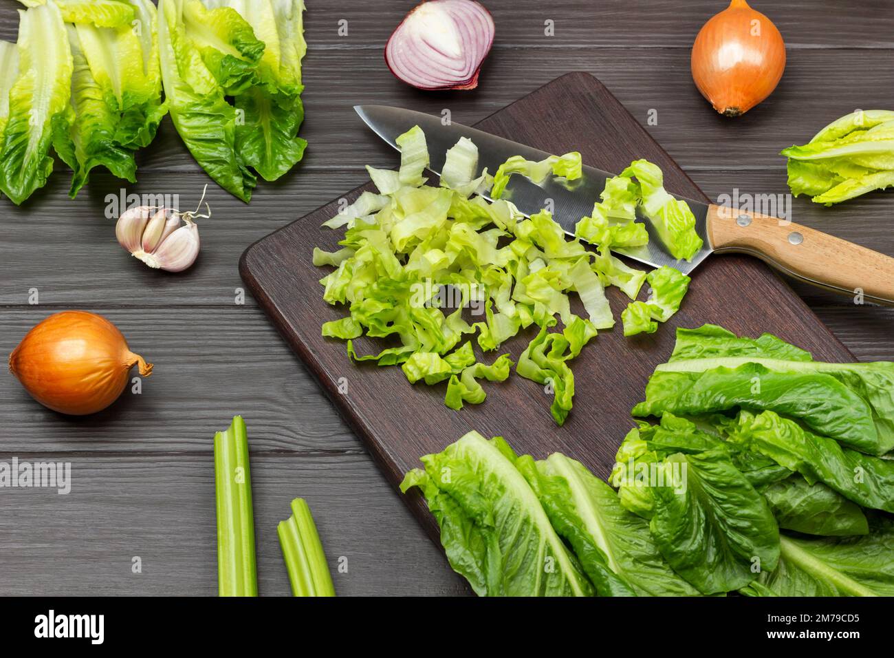 Chopped lettuce leaves and knife on cutting board. Vegetables on table ...