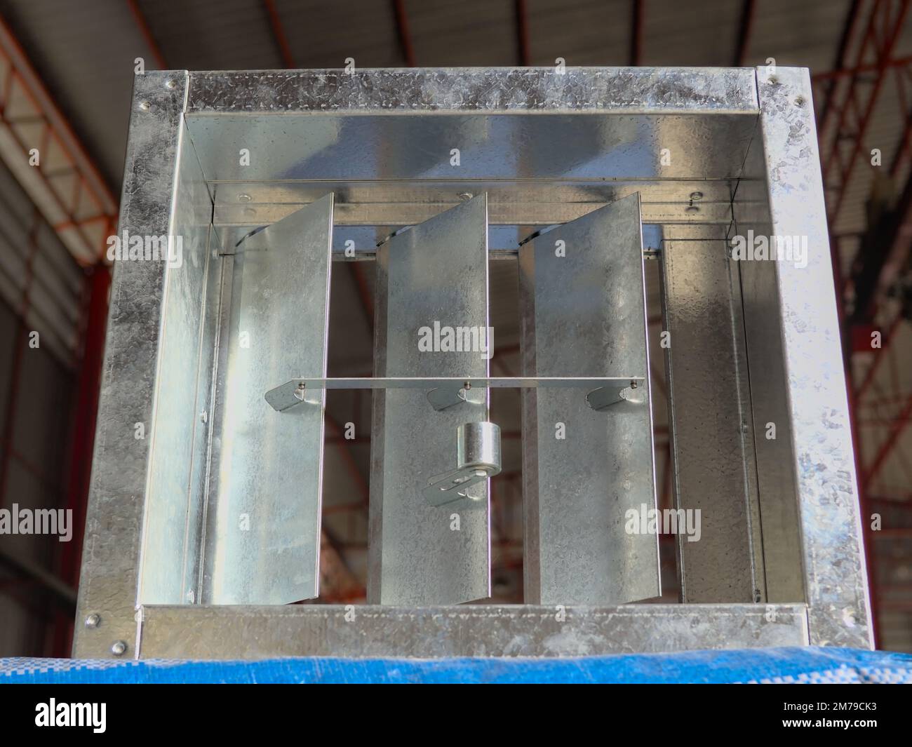 A metallic Volume Damper with its flaps partially open against blurred ...