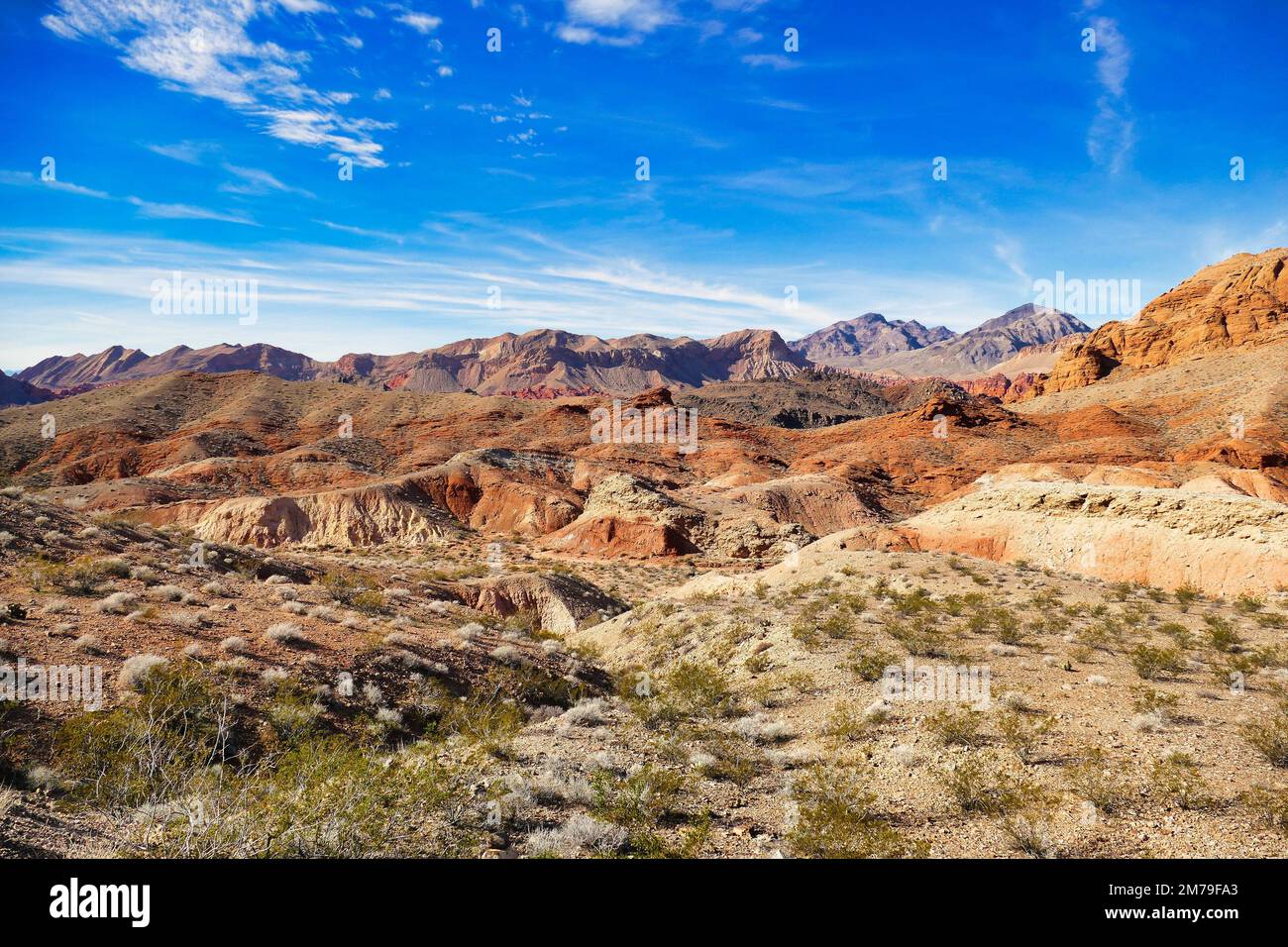 Arid desert landscape with eroded red rocks, sparse vegetation and dark ...