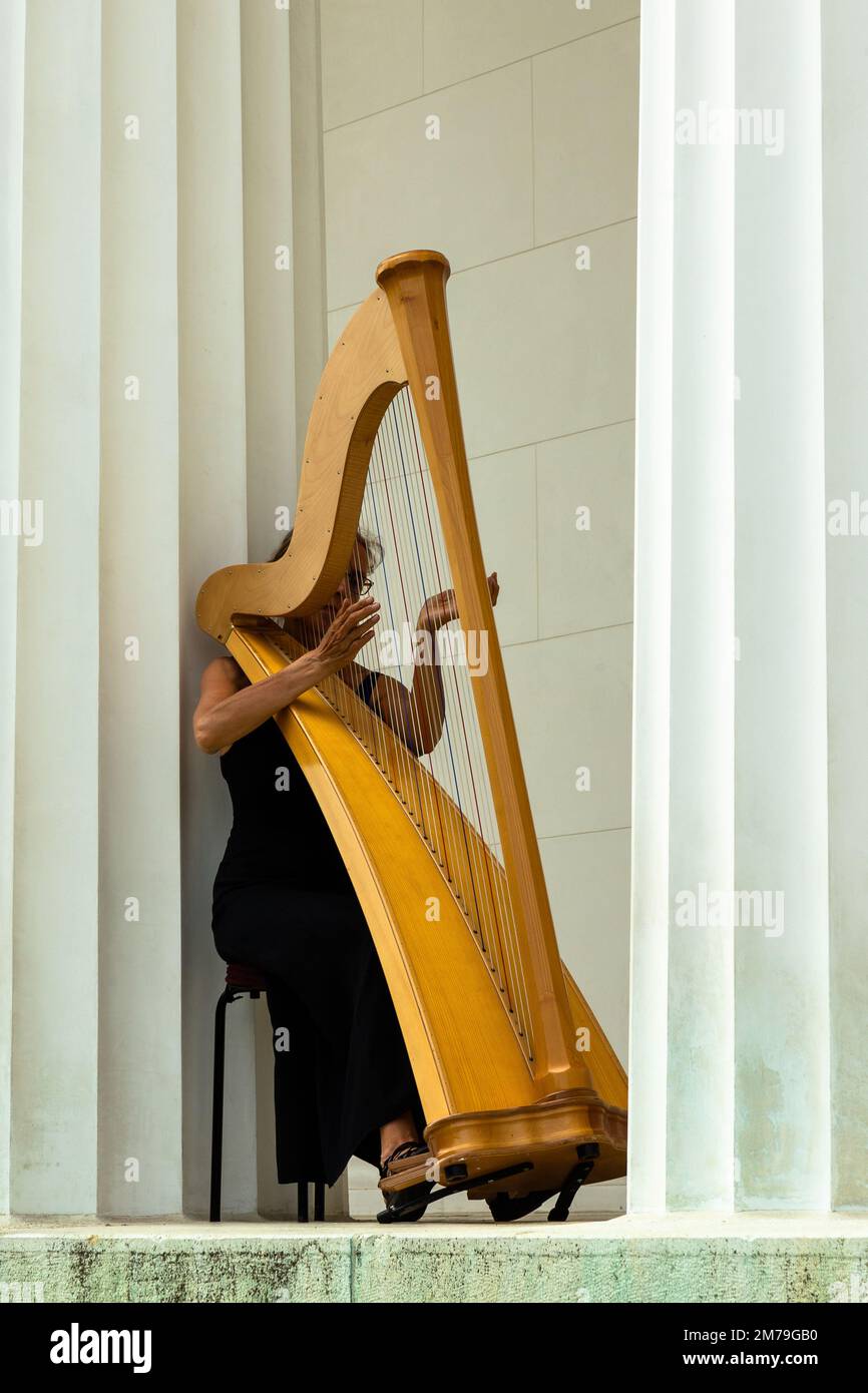 Lone female harpist, playing her harp between the columns of the ...