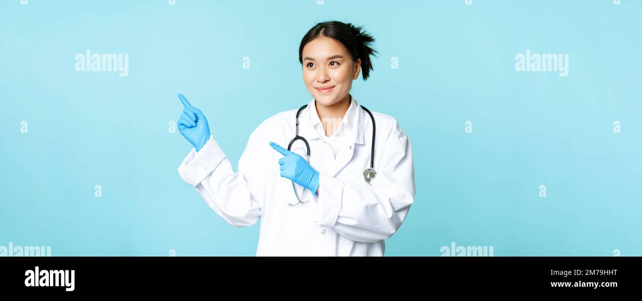 Smiling asian doctor, medical worker in uniform, pointing and looking ...