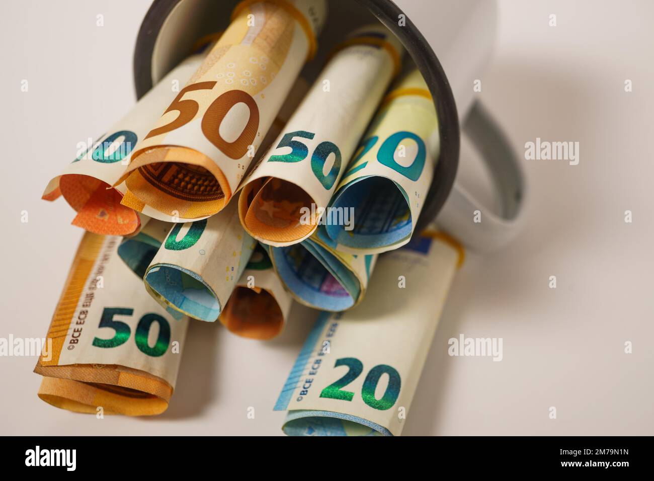Rolled euro banknotes in a white cup with white background and copy ...