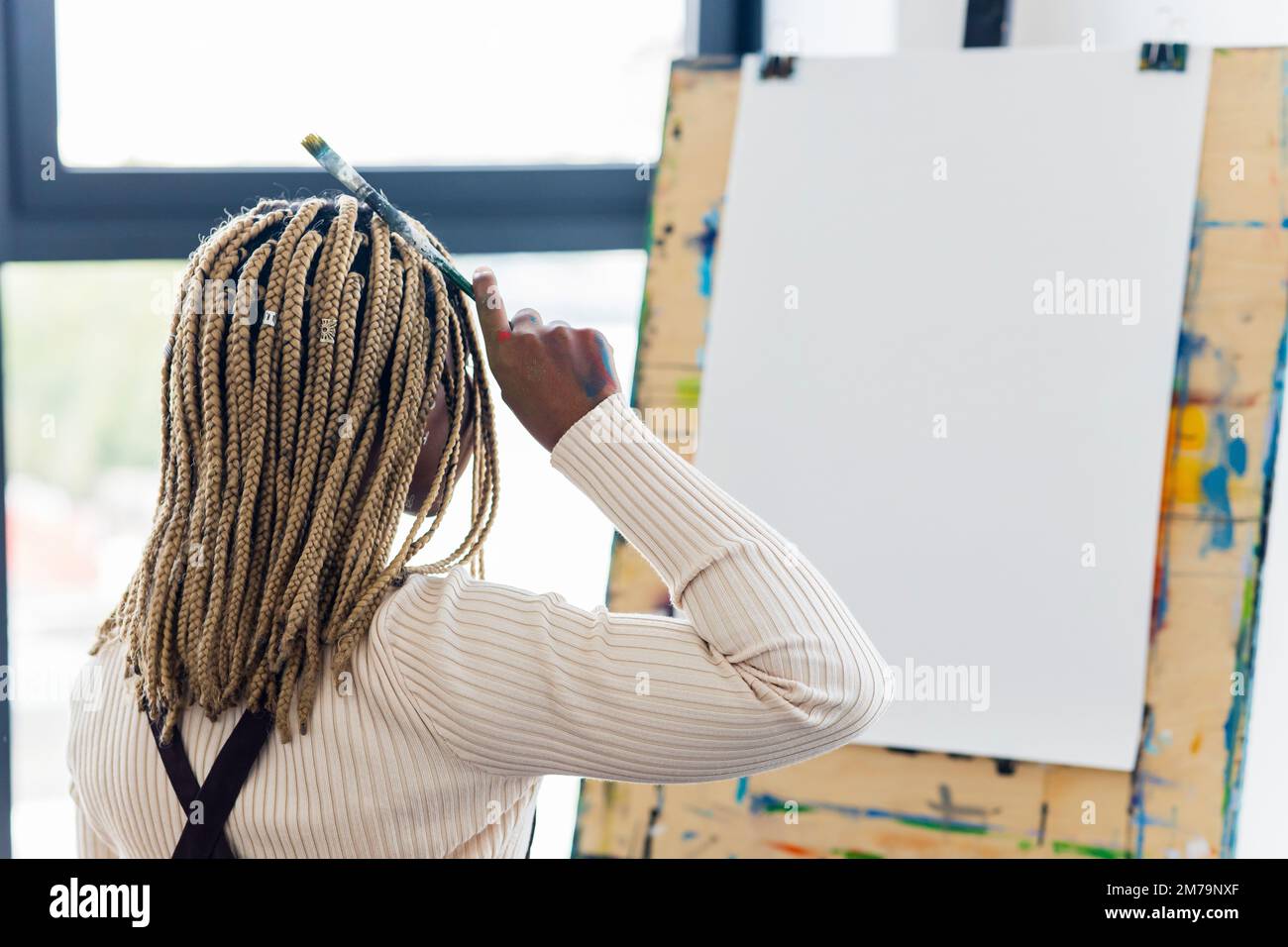 african american woman sitting next to blank white canvas on easel in ...
