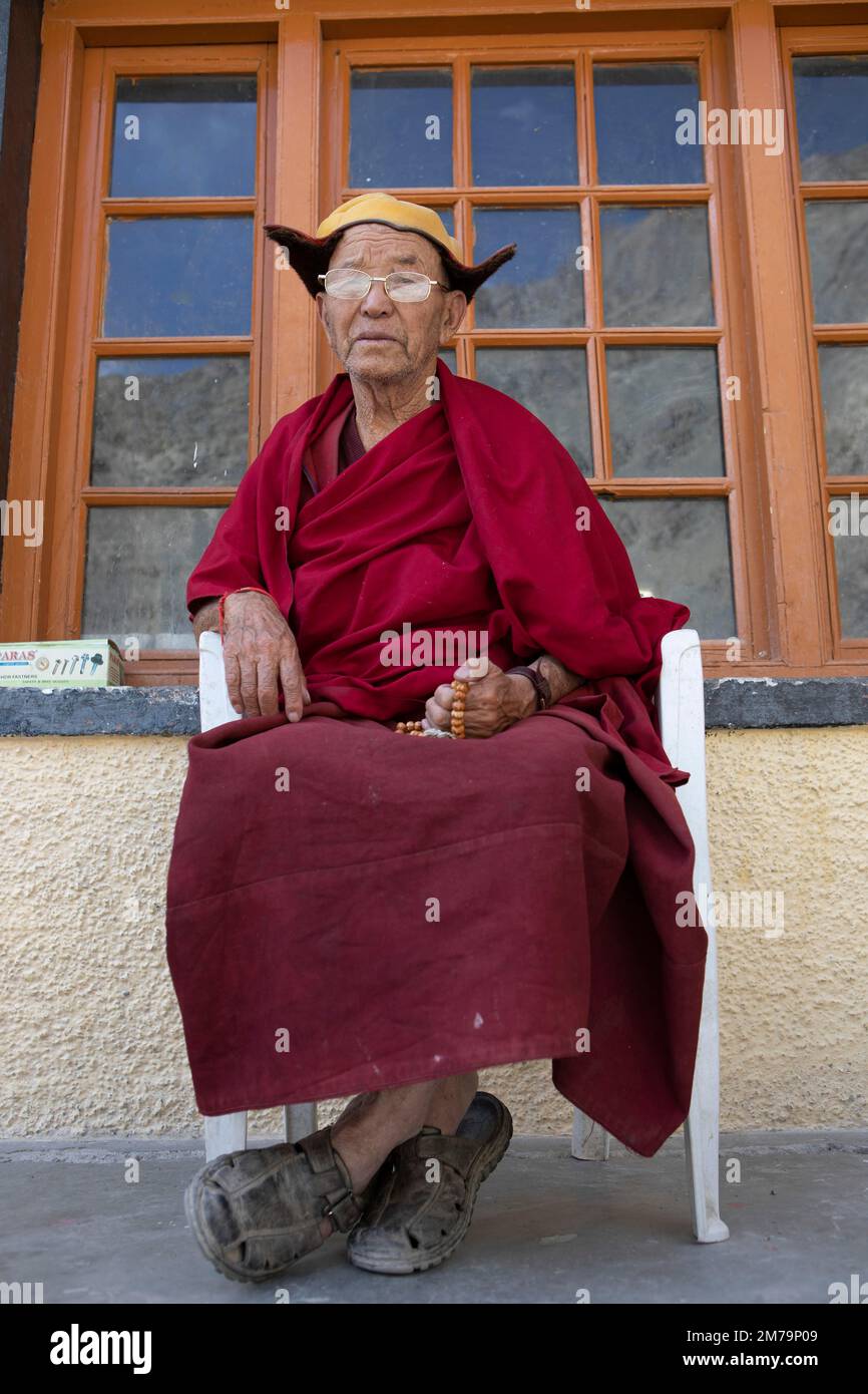 Monk sitting on garden chair, Buddhist Yellow Cap Monastery Rizong or ...