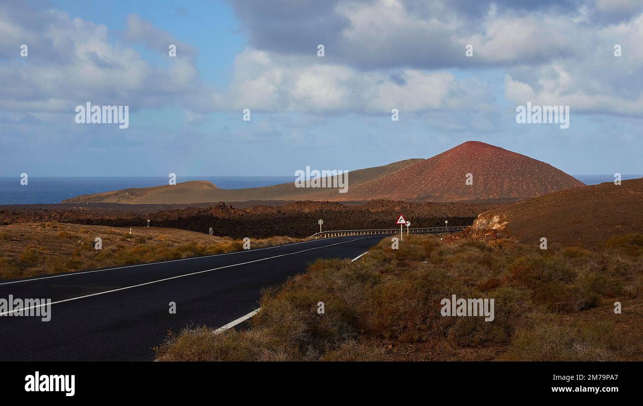 Brown lava scree, reddish brown lava hill, asphalt road, Timanfaya ...