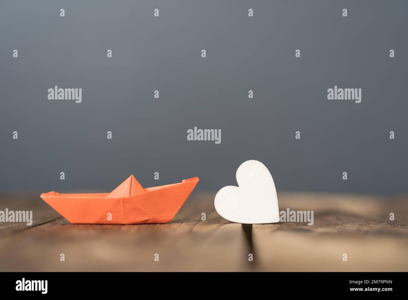 close-up of an orange miniature origami ship with a wooden heart on ...