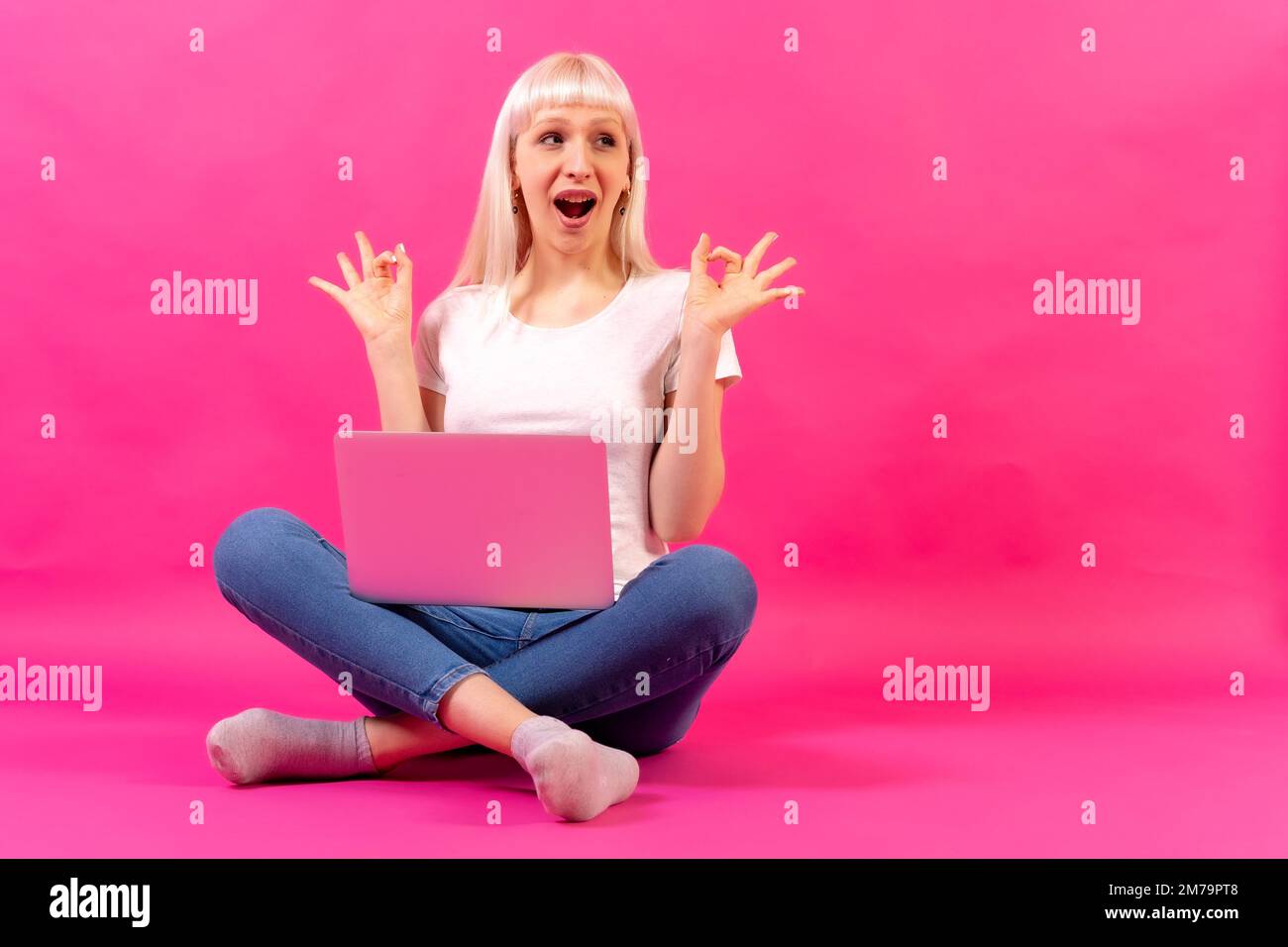 Blonde caucasian girl with a computer, studio shot on pink background ...