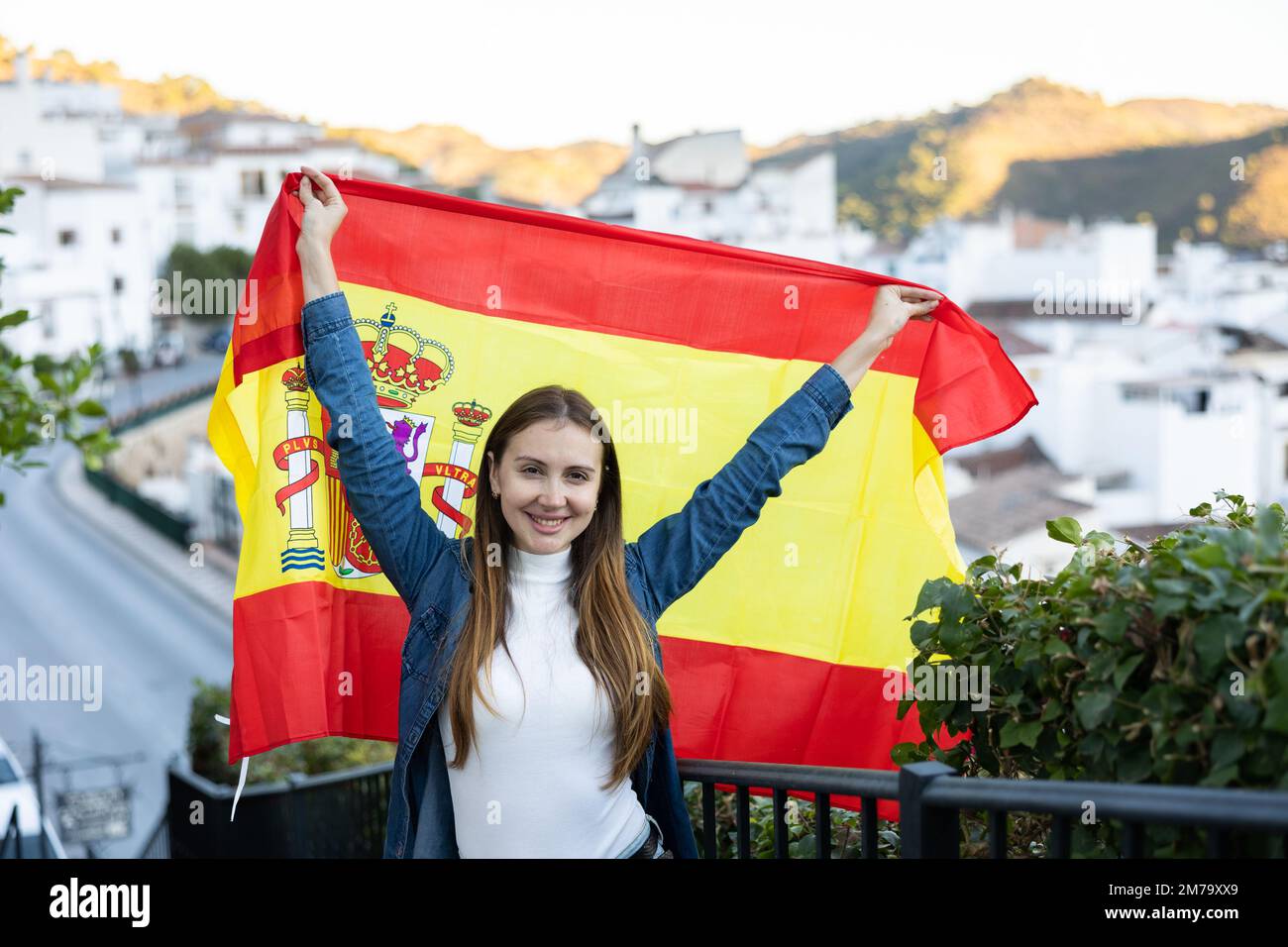 Cheerful young female traveler waving Spanish flag on city street ...