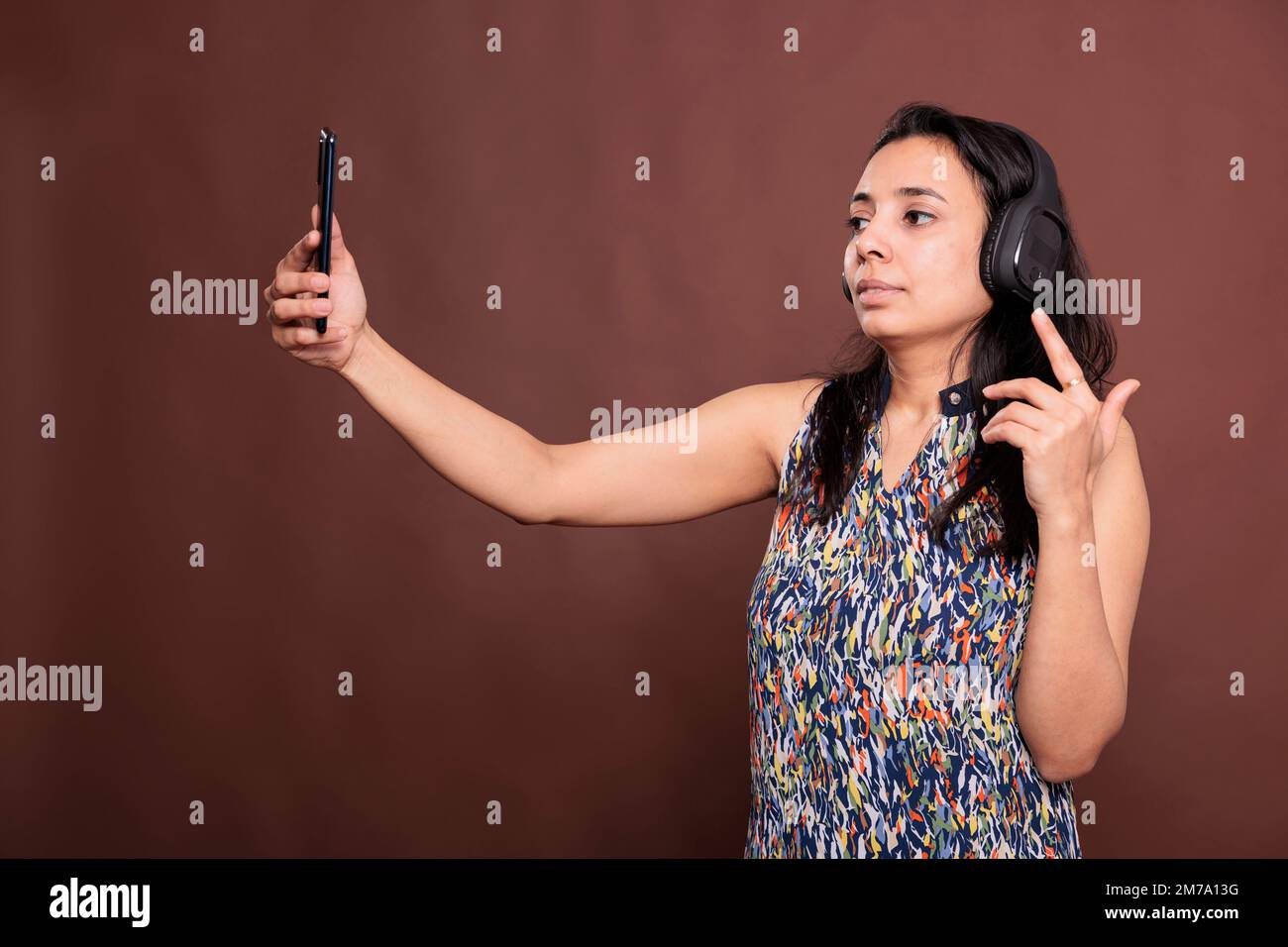 Indian woman in headphones having videocall on smartphone, talking on ...