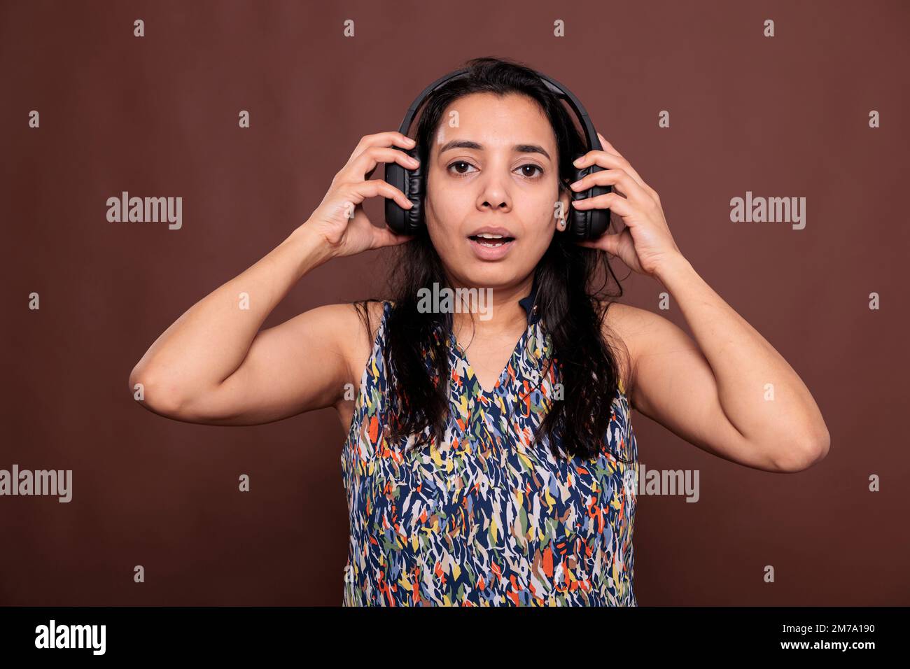 Indian woman taking off wireless headphones, looking at camera with ...