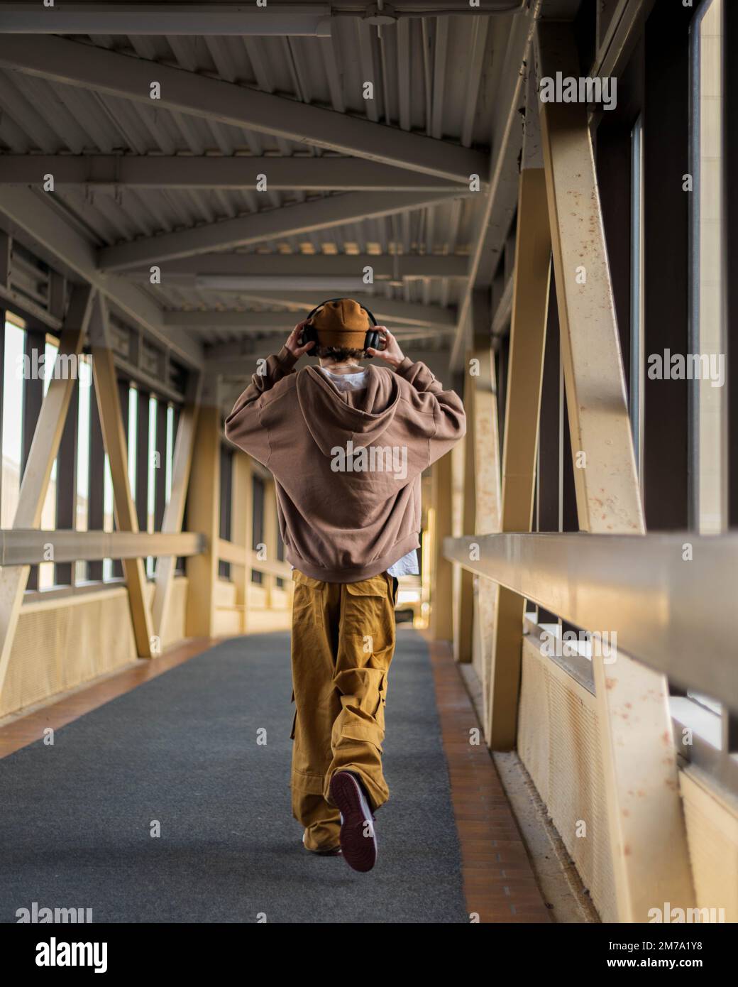 A back view of a stylish male with headphones walking on a bridge Stock ...