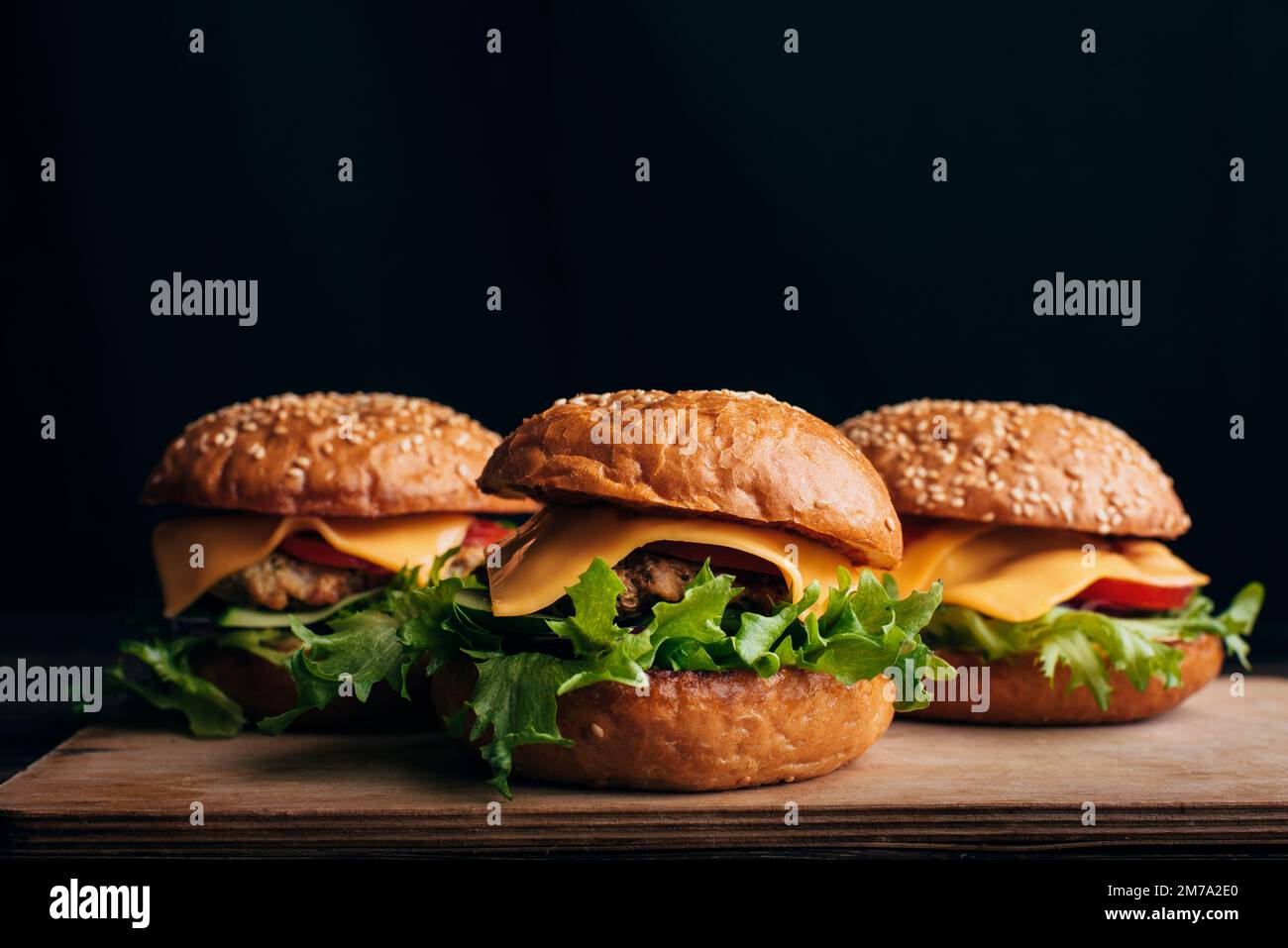 three homemade hamburgers with meat, cheese, lettuce and tomatoes on a ...