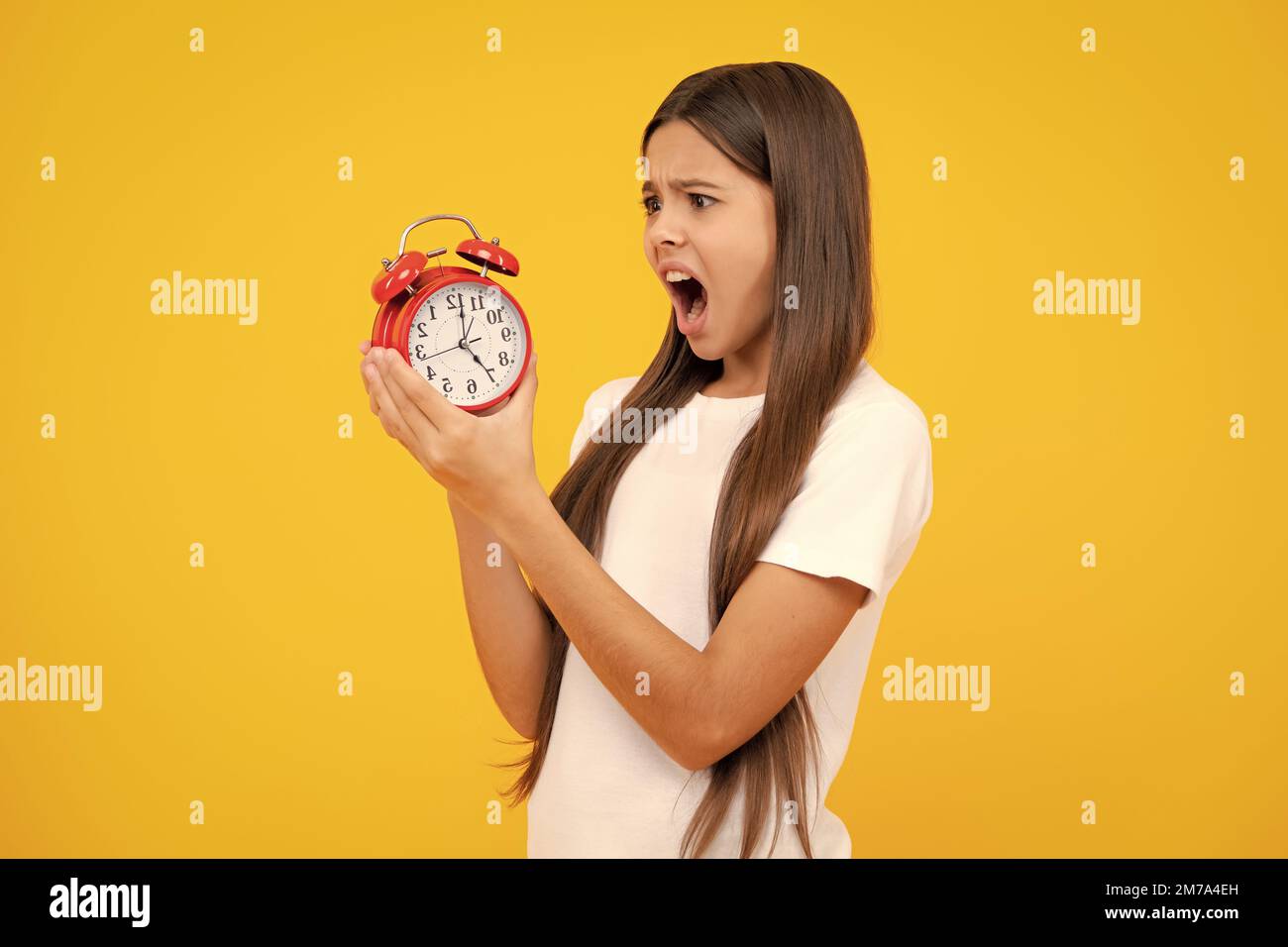 Teen girl holding clock over yellow background. Early morning, daily ...