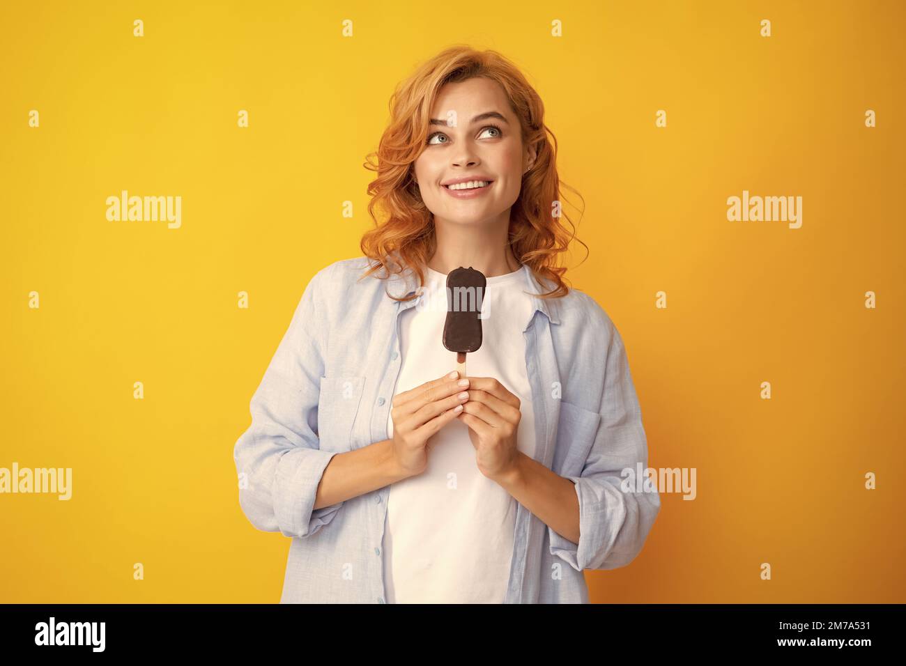 Young woman eat ice creams with chocolate glaze on yellow background ...