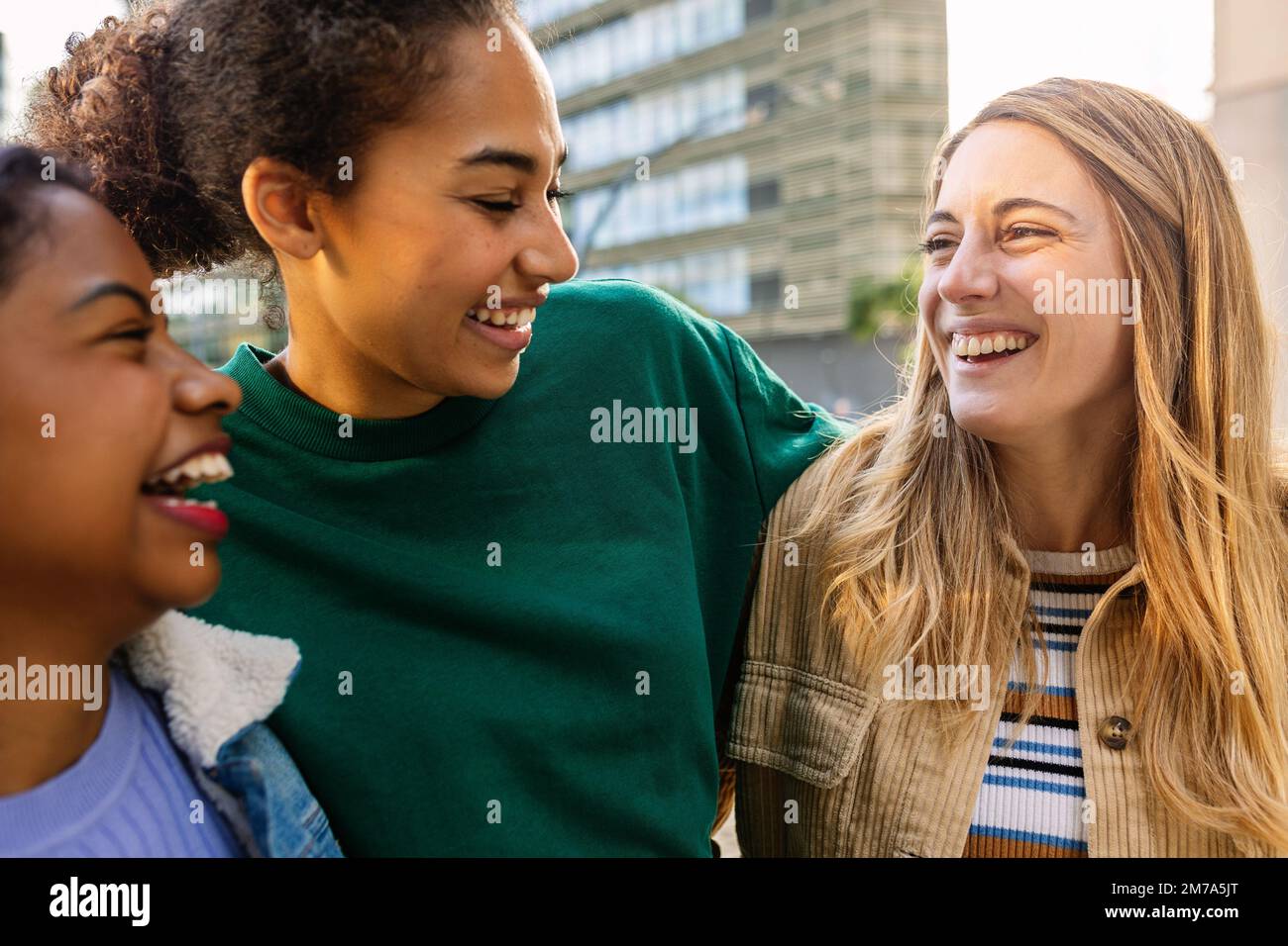 Three young women hugging and laughing outdoors Stock Photo - Alamy