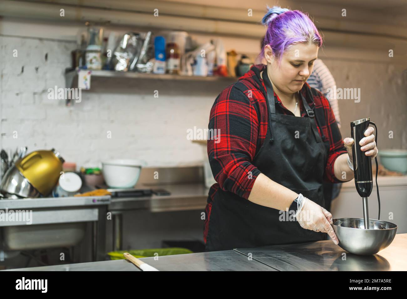 A female baker with purple hair blending products in a metal bowl on a ...